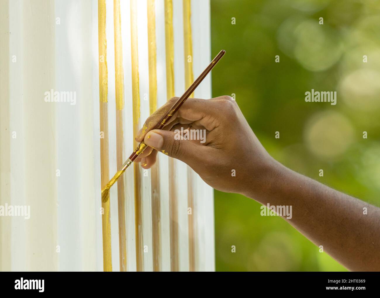 Male hand painting the vertical lines on the wall with a golden paint ...