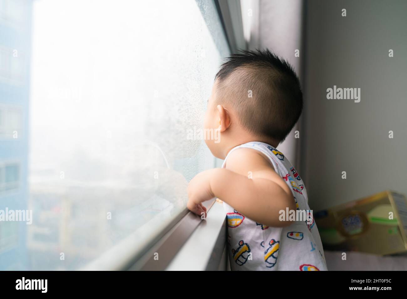 Happy baby boy stand near window looking to rainy outside from ...