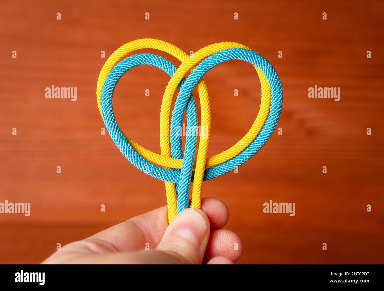 Heart symbol made of twisted blue and yellow braided cords in hand ...