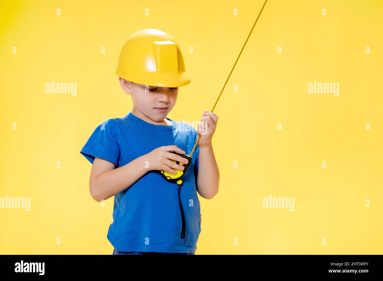 A little boy in a protective construction helmet measures with a tape ...