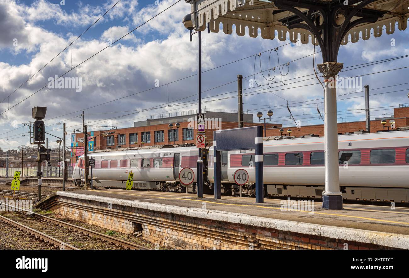 A train rests at a historic railway station platform. Buildings are in ...