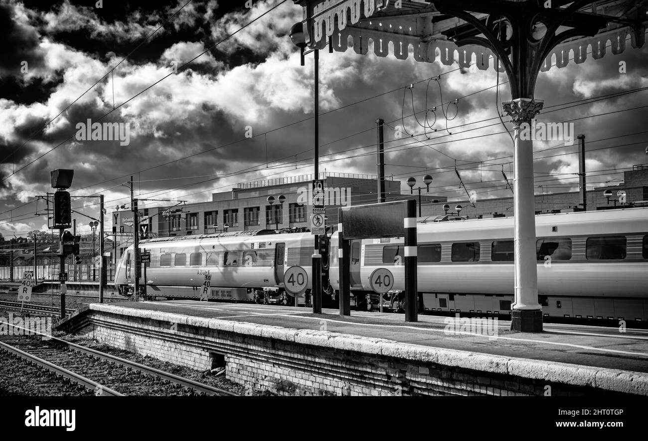 A train rests at a historic railway station platform. Buildings are in ...