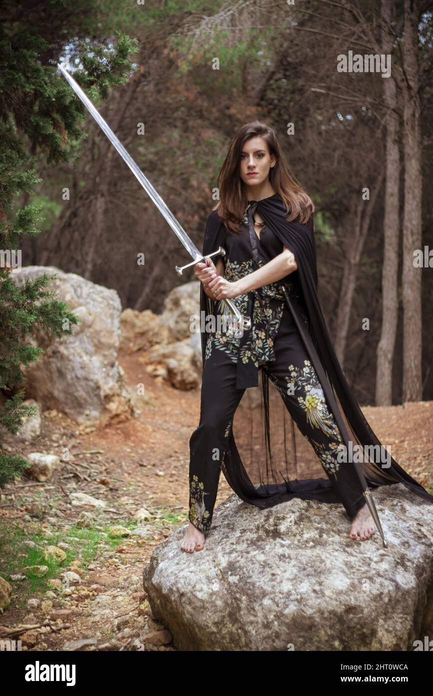 Vertical shot of a powerful young female with a sword posing in a ...