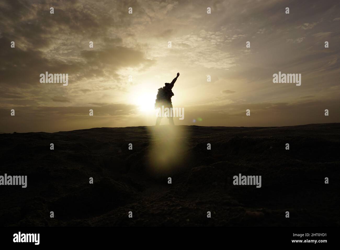 View of a man standing on the top of a hill with his arm up under the ...