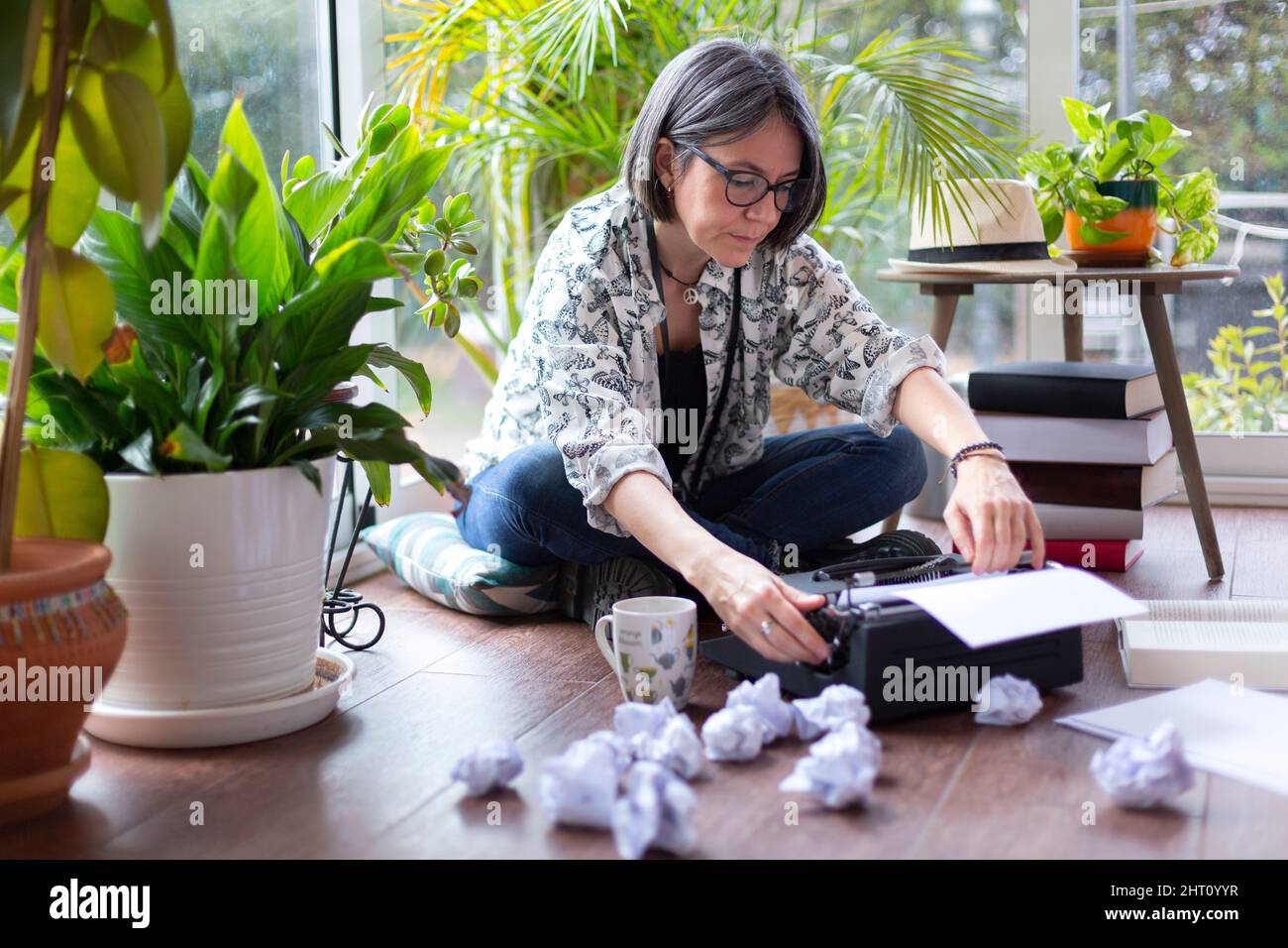 Adult female writer putting new blank sheet of paper on typewriter next ...