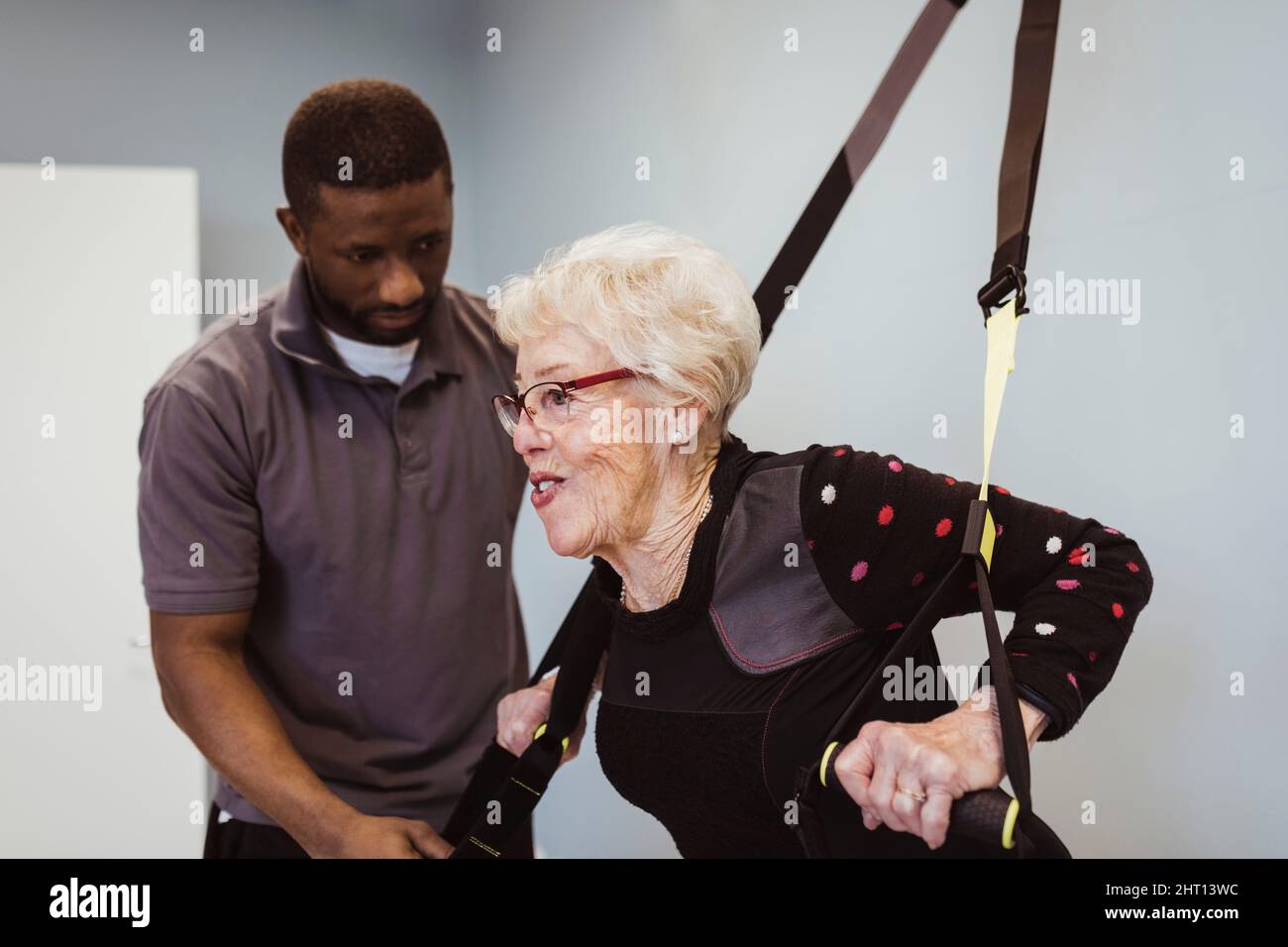 Elderly woman stretching resistance band by male healthcare worker at ...