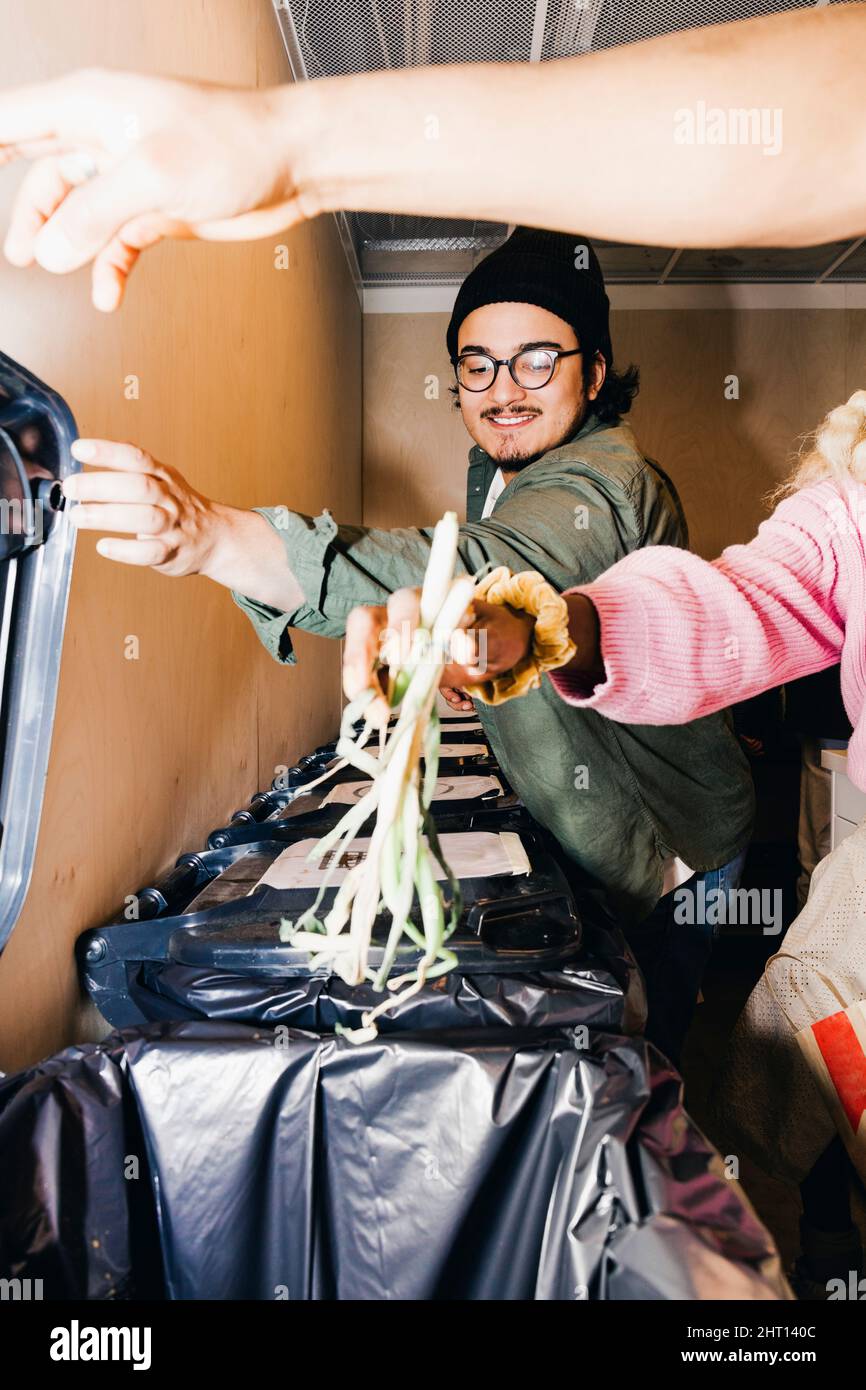 Young woman putting leftovers while friends opening garbage bin at ...