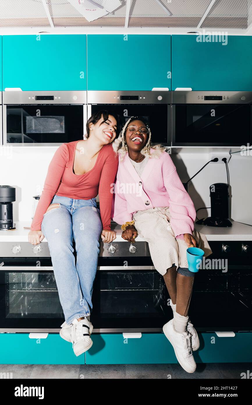 Happy young women sitting on kitchen counter in college dorm Stock ...