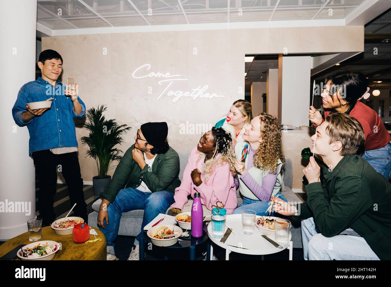 Smiling young man photographing multiracial friends holding props while ...