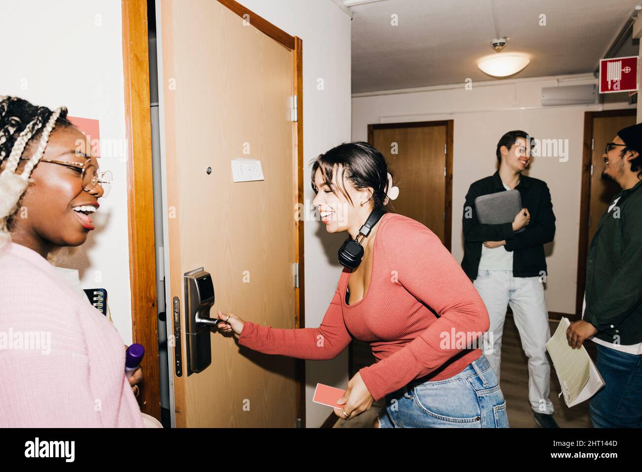 Happy young woman opening door while multiracial friends at corridor in ...