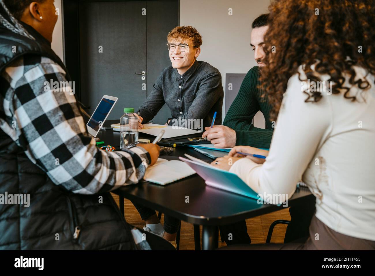 Smiling multiracial adult students studying together at table in ...