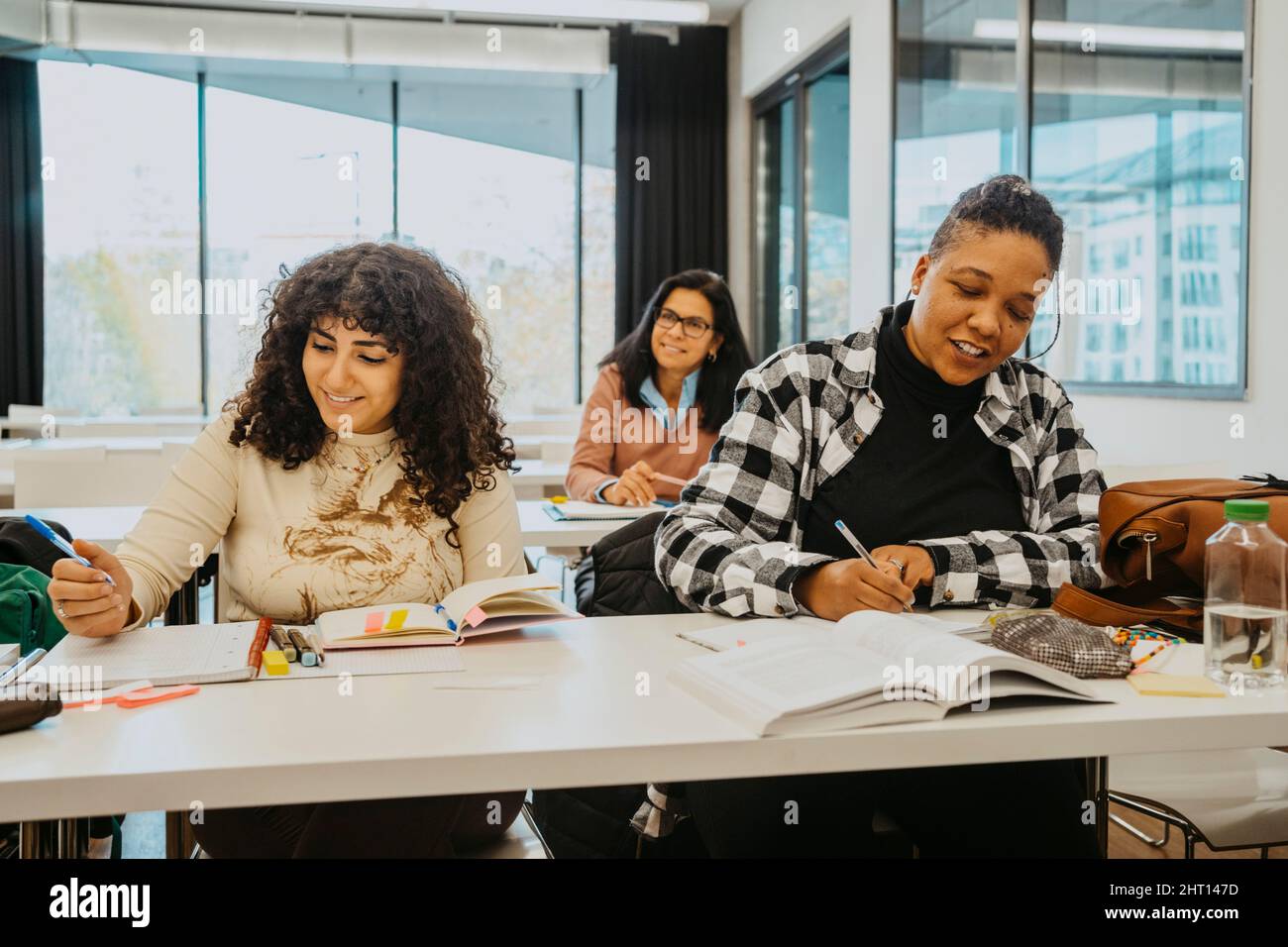 Female students writing while sitting at desks in classroom Stock Photo ...