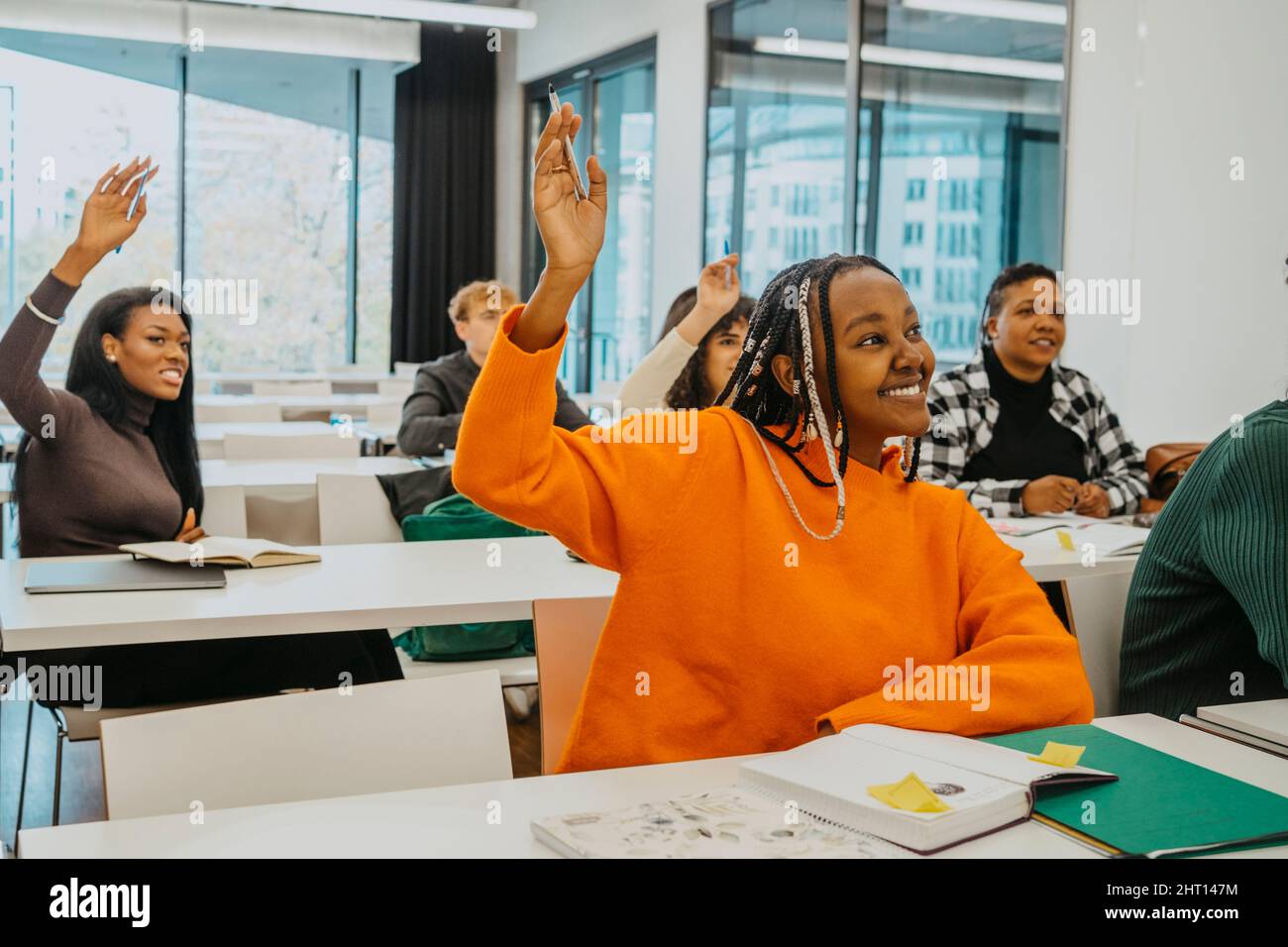 Female students raising hands while sitting in classroom Stock Photo ...