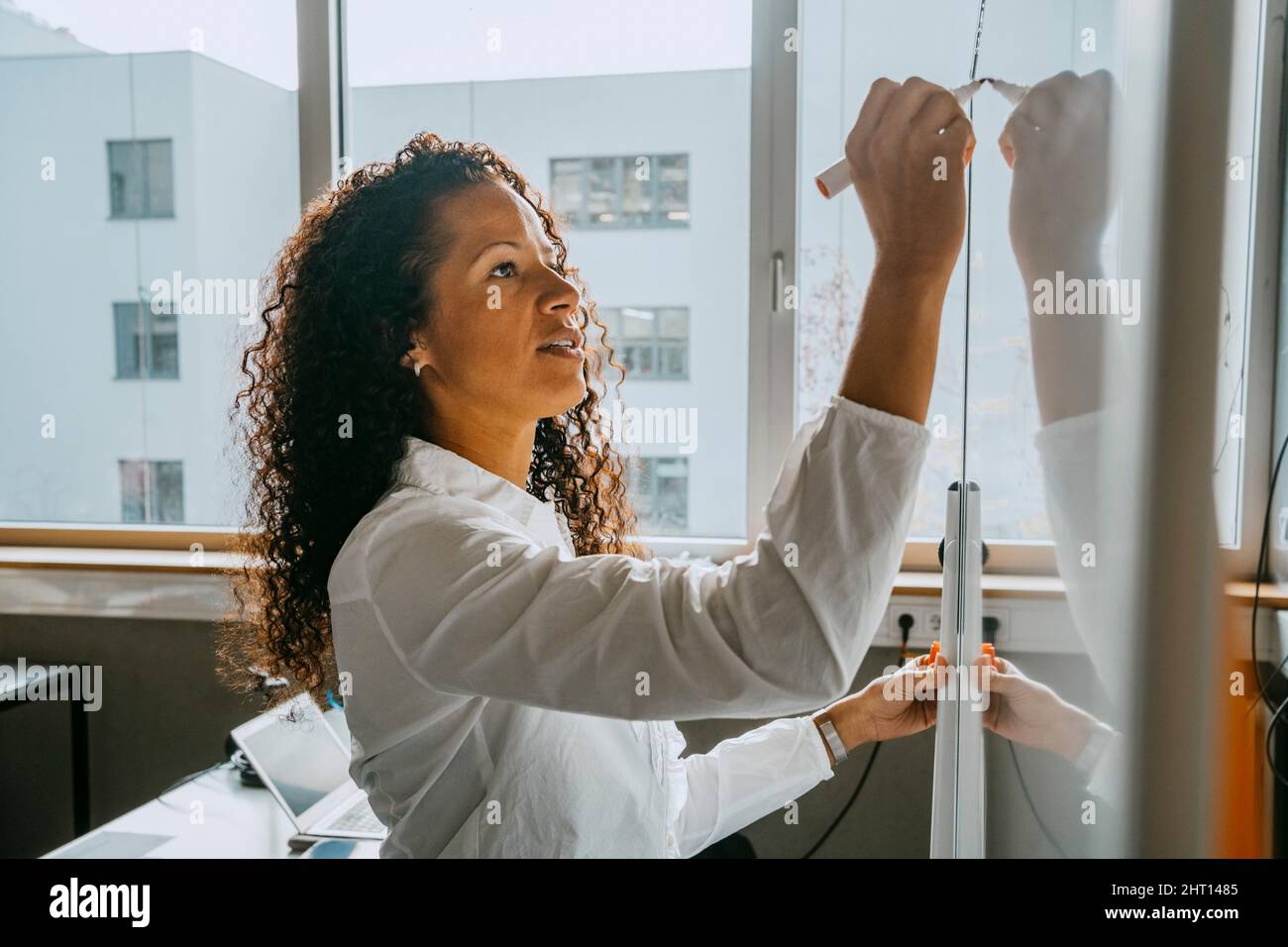 Side view of teacher writing on whiteboard with felt tip pen in ...