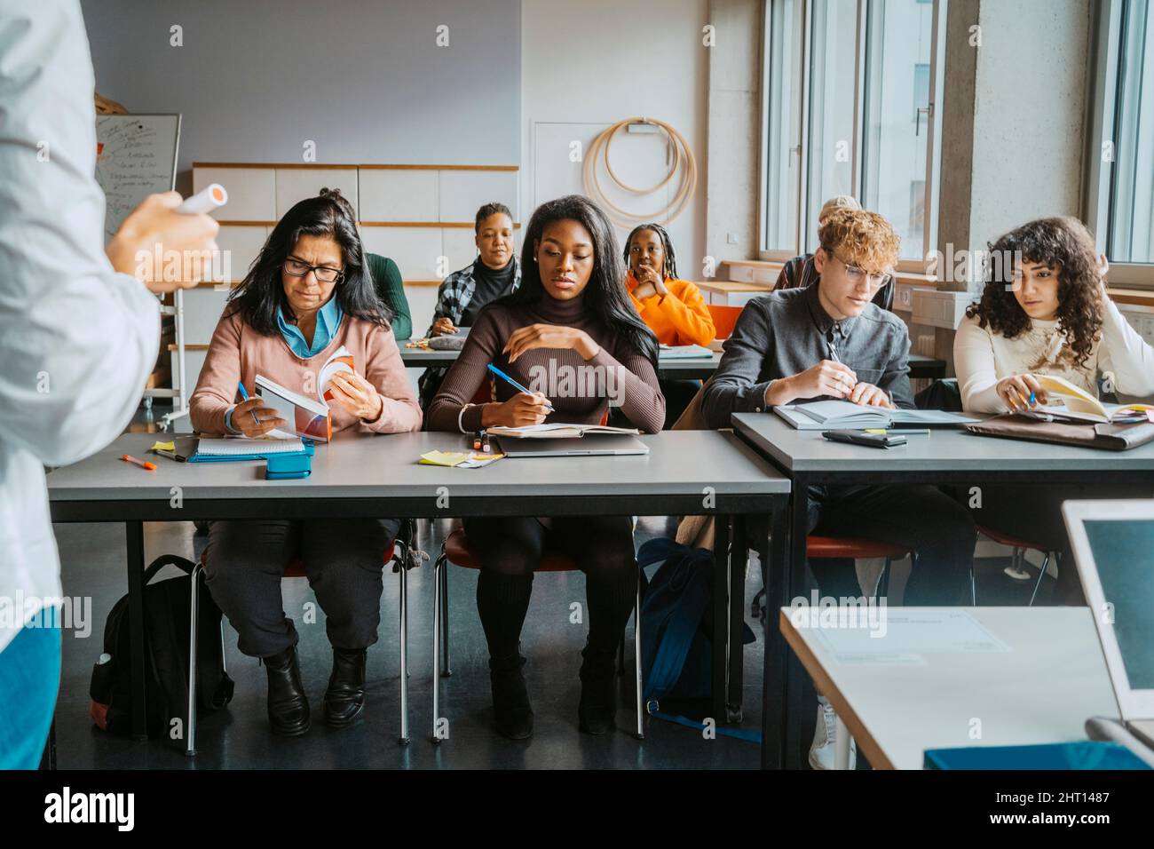 Multiracial students sitting at desk while learning from teacher in ...
