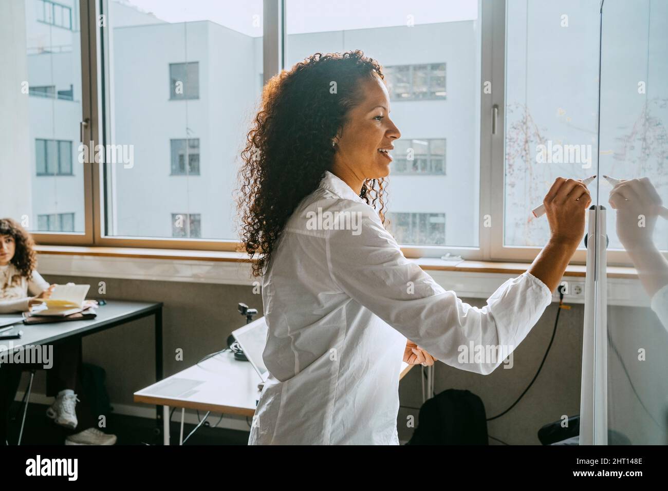 Side view of professor writing on whiteboard with felt tip pen in ...