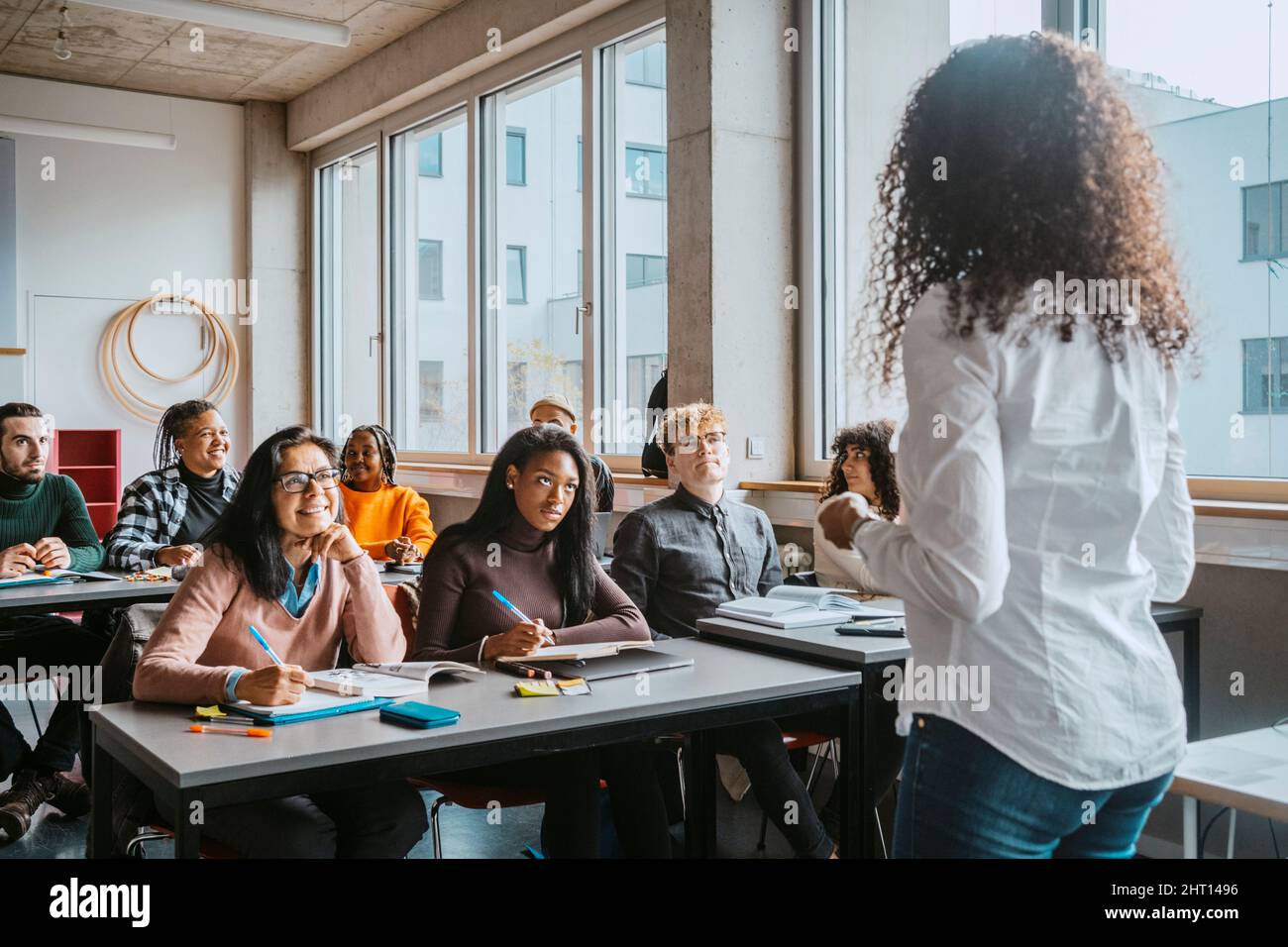 Multiracial students listening to professor teaching in classroom at ...