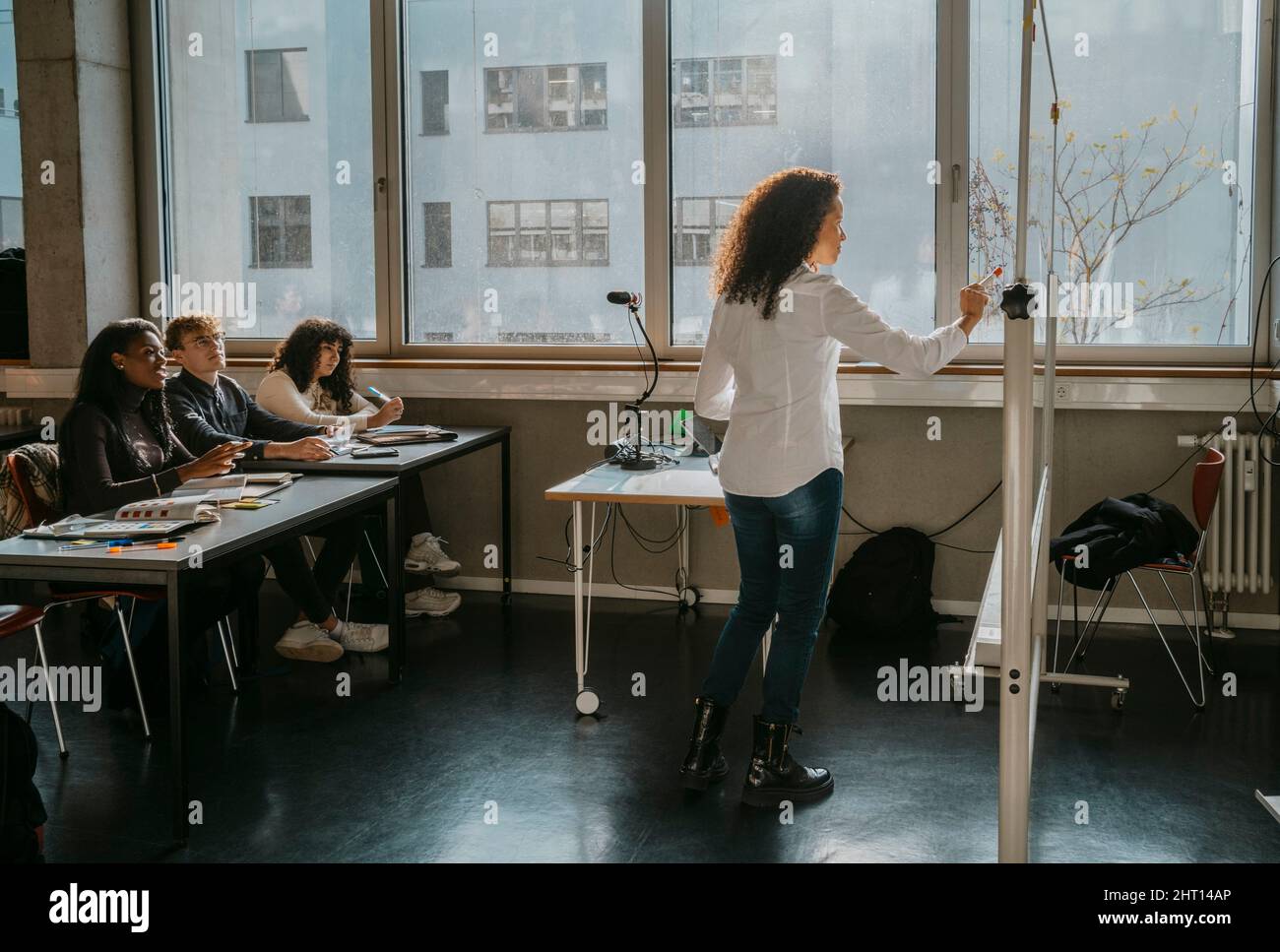 Professor writing on whiteboard while teaching university students in ...
