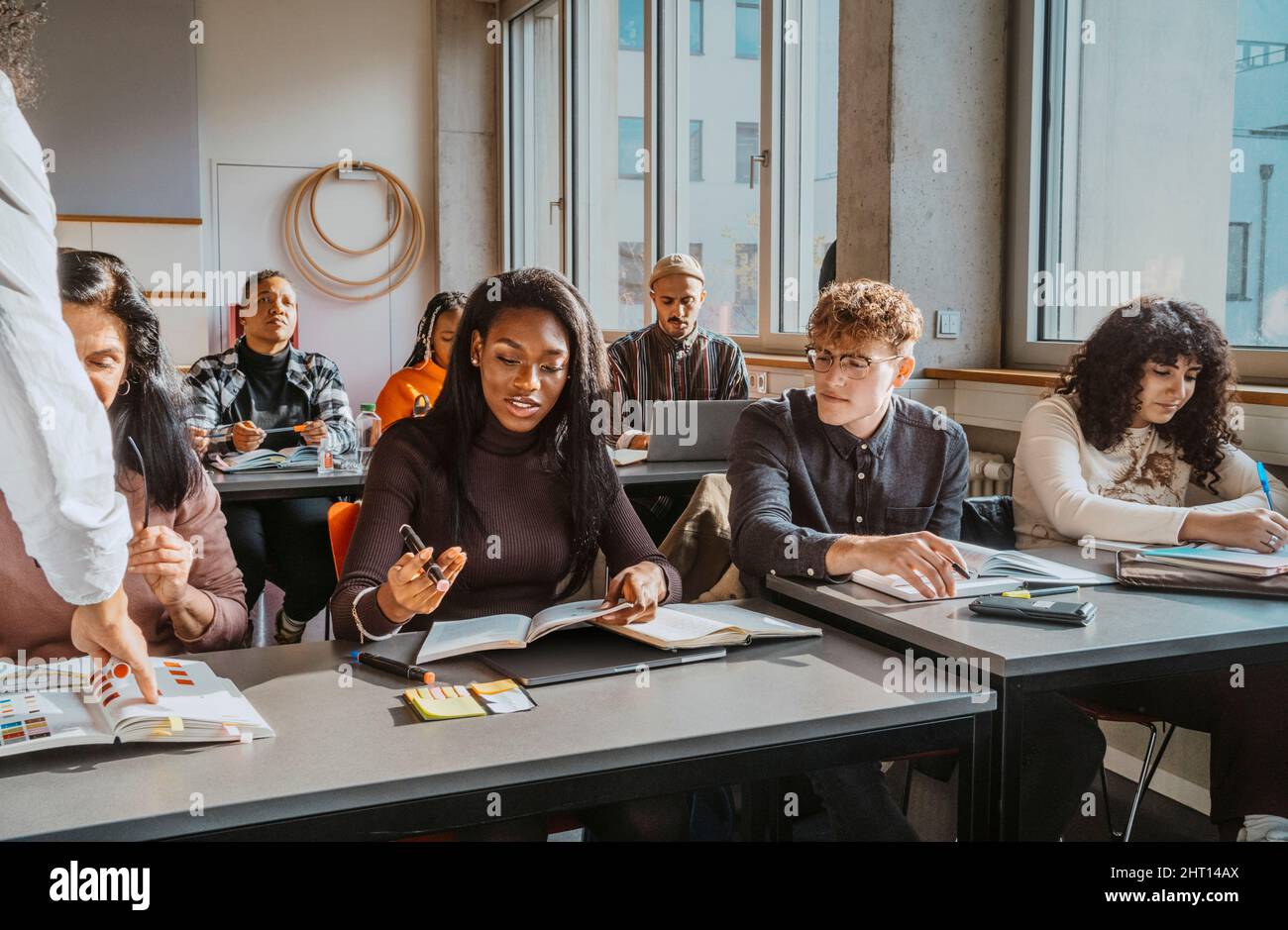 Multiracial students sitting at desk while learning from professor in ...