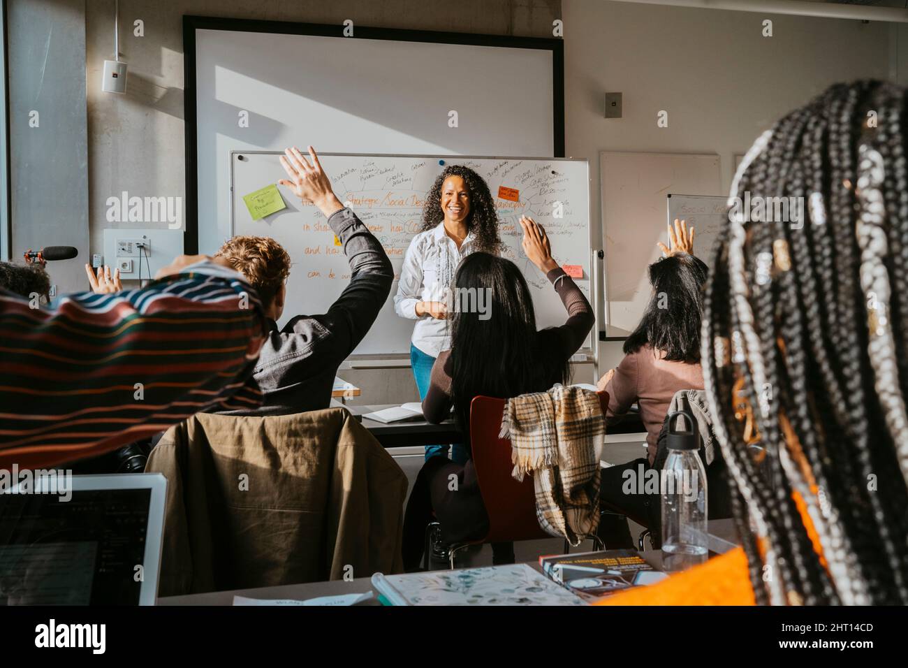 Smiling professor looking at university students sitting with hands ...