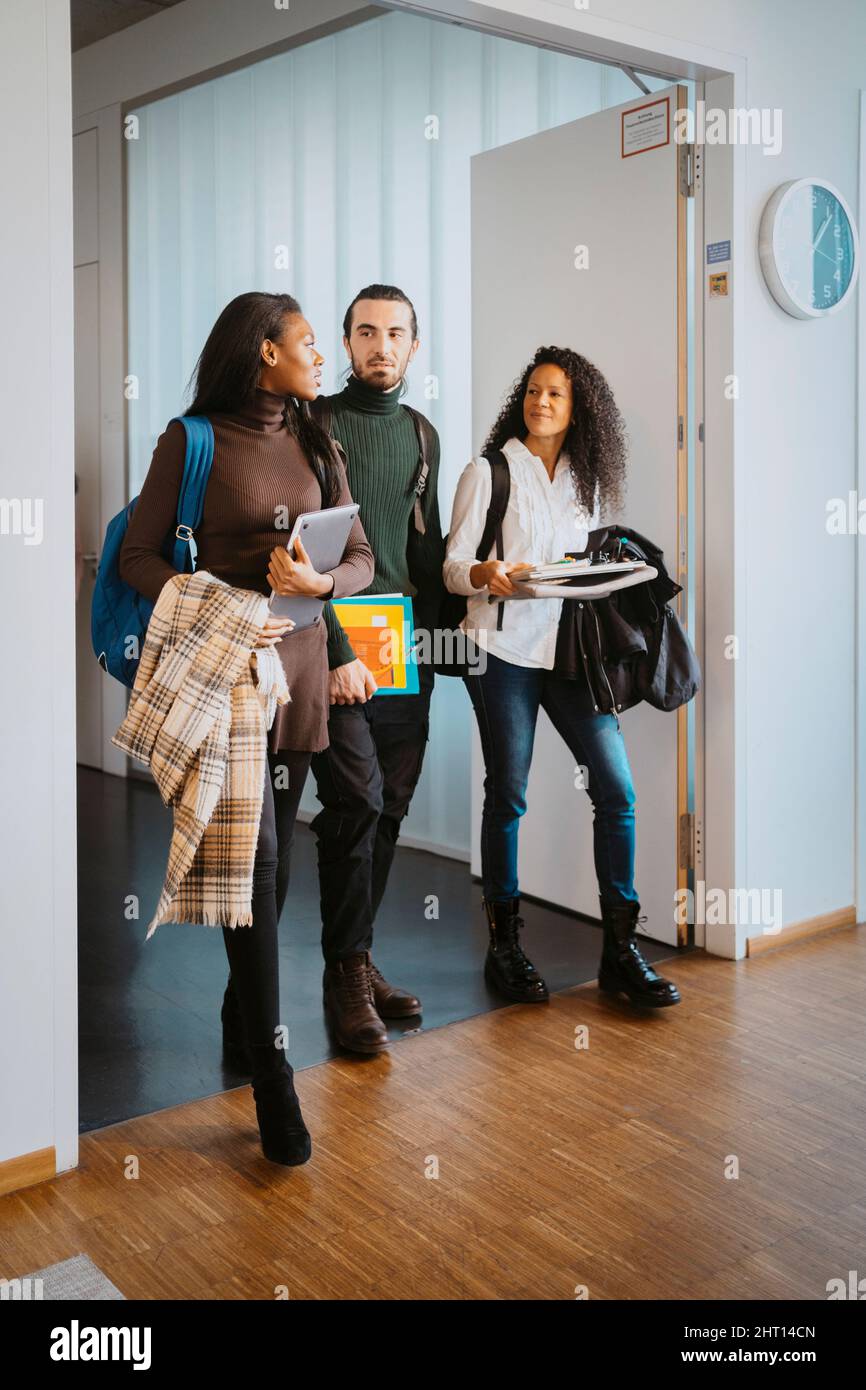 Smiling professor walking with students in classroom at university ...