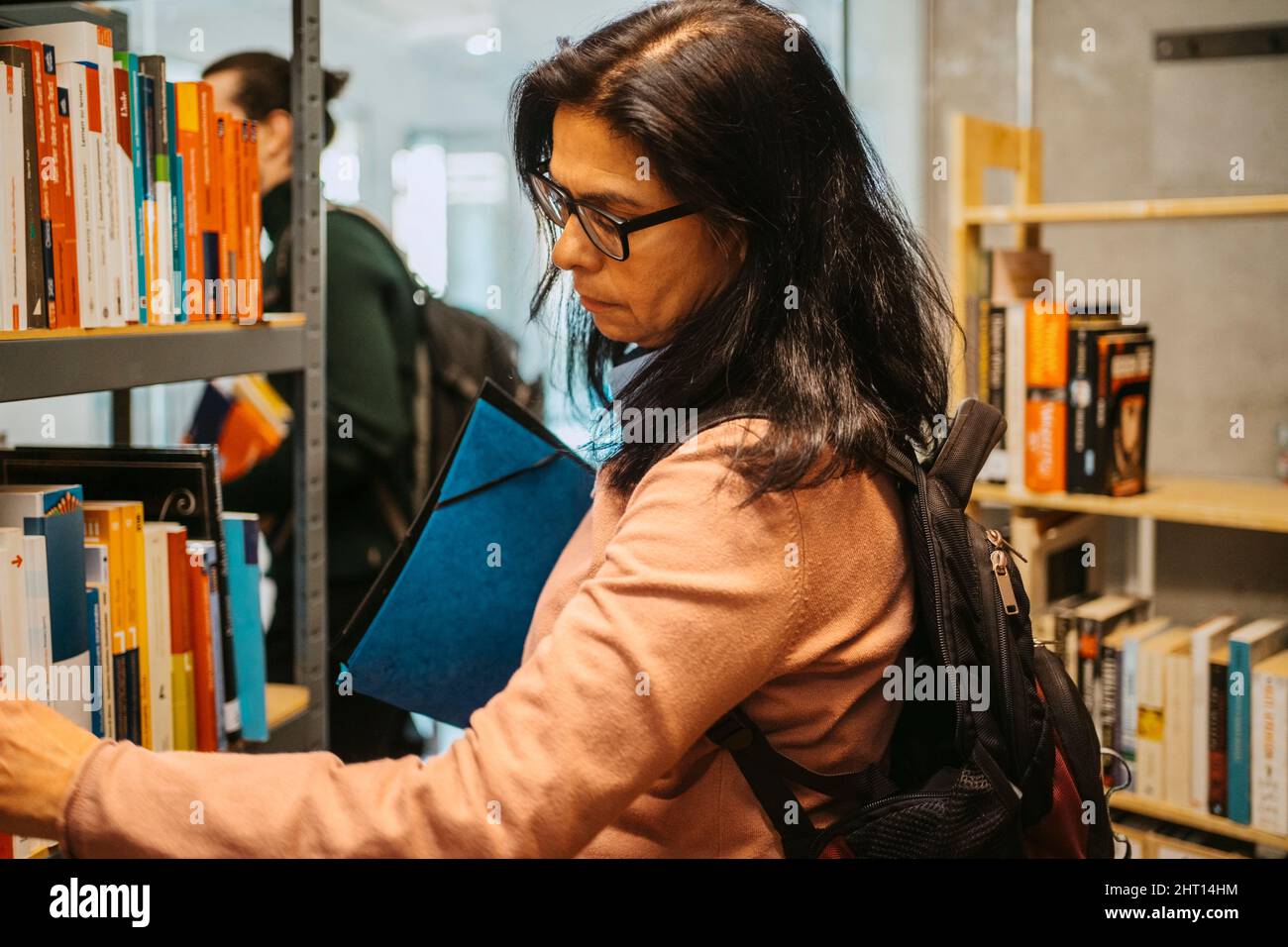 Side view of mature female student searching book on rack in college ...