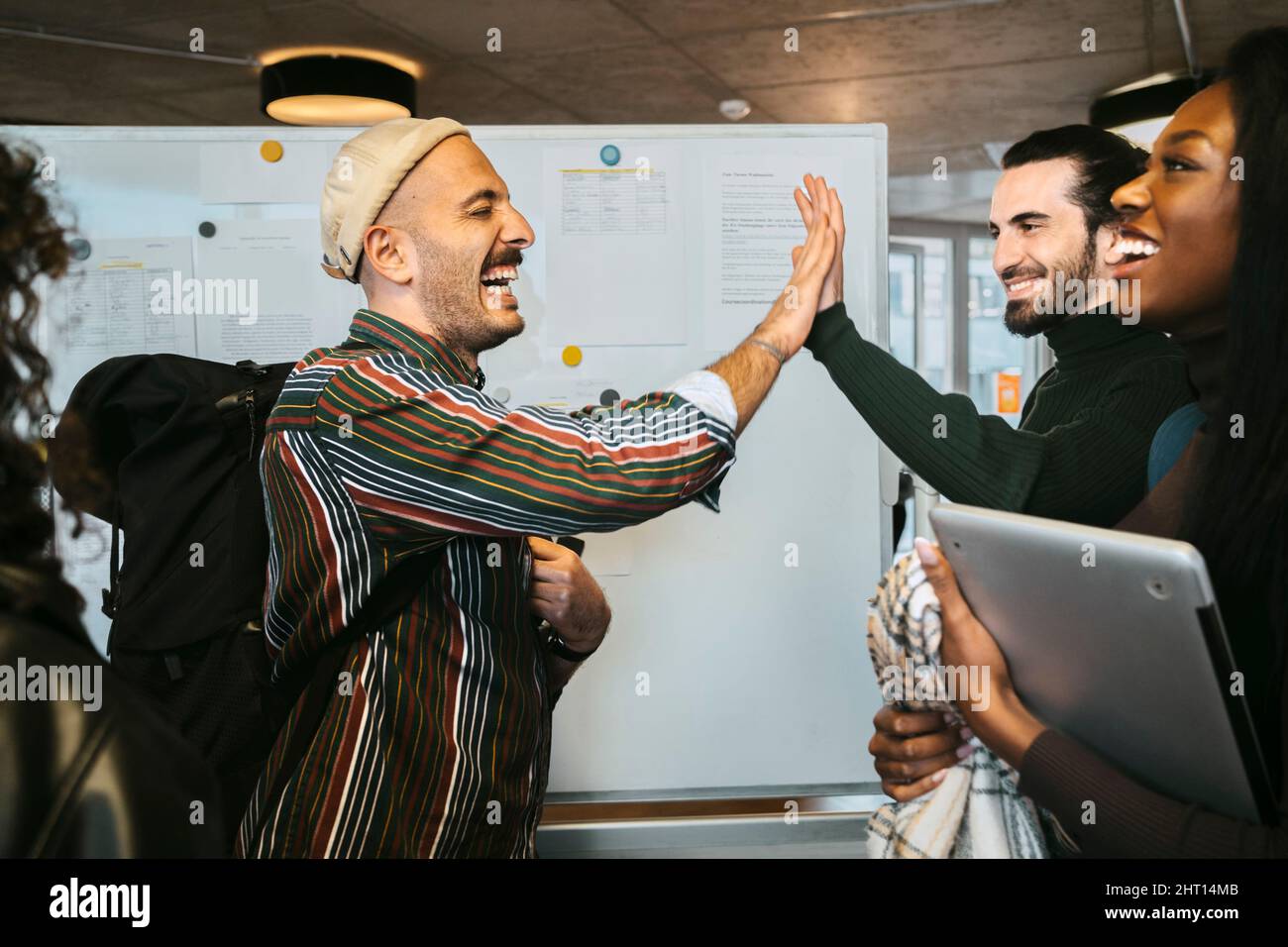Cheerful male friends giving high-five by woman laughing in college ...