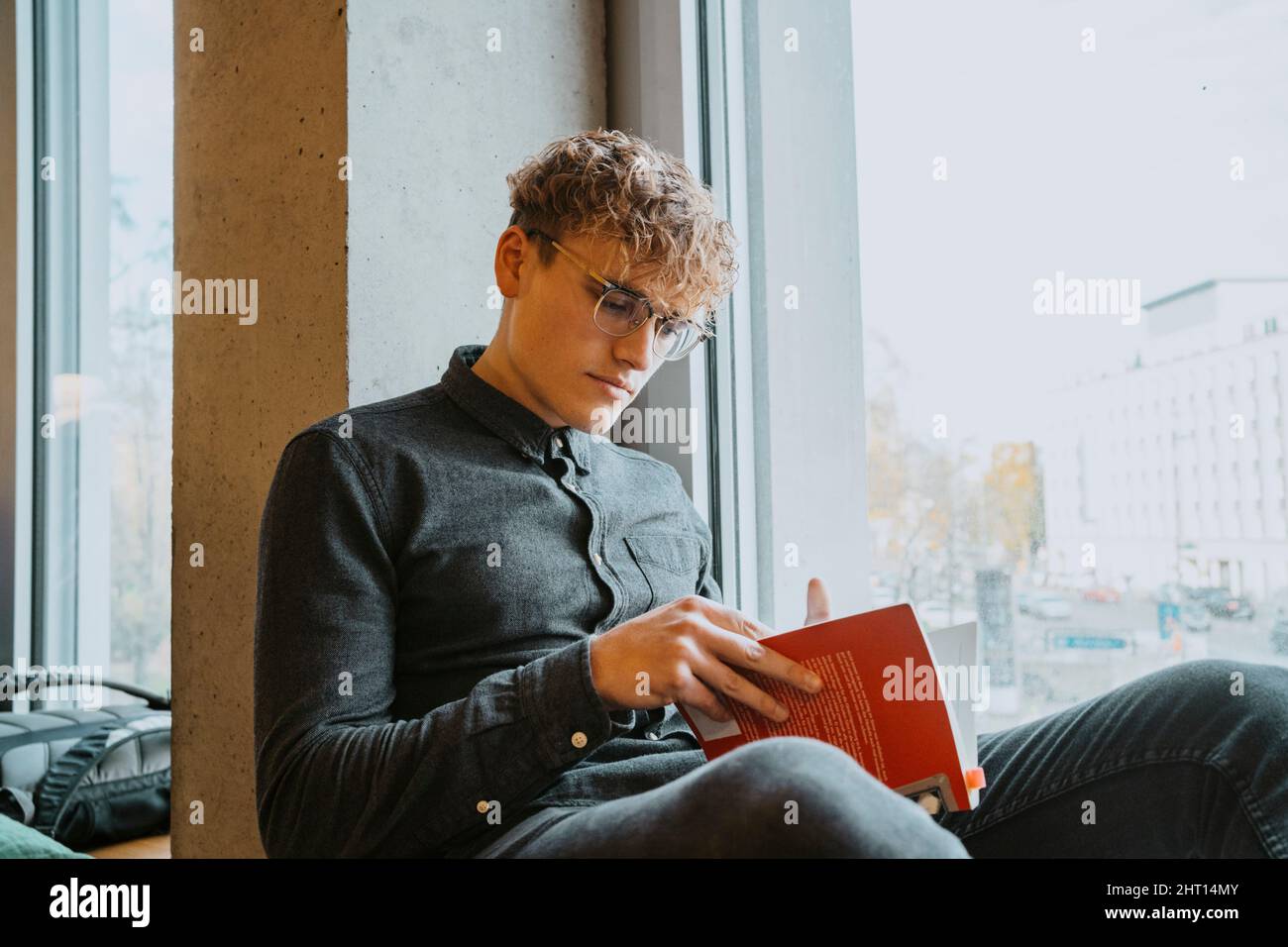 Young blond man reading book by window in university cafeteria Stock ...