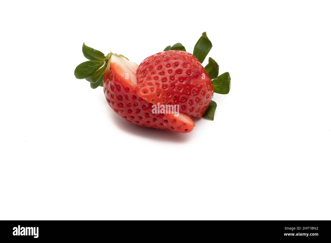 A whole strawberry with its green leaves, cut in half. Isolated on ...