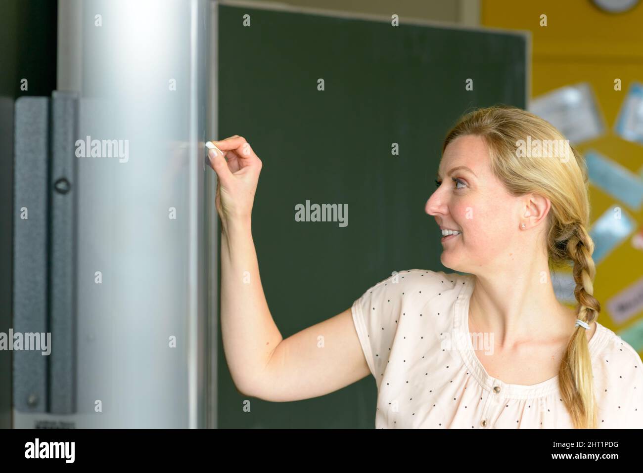 Motivated happy school teacher writing on the chalkboard with a smile ...