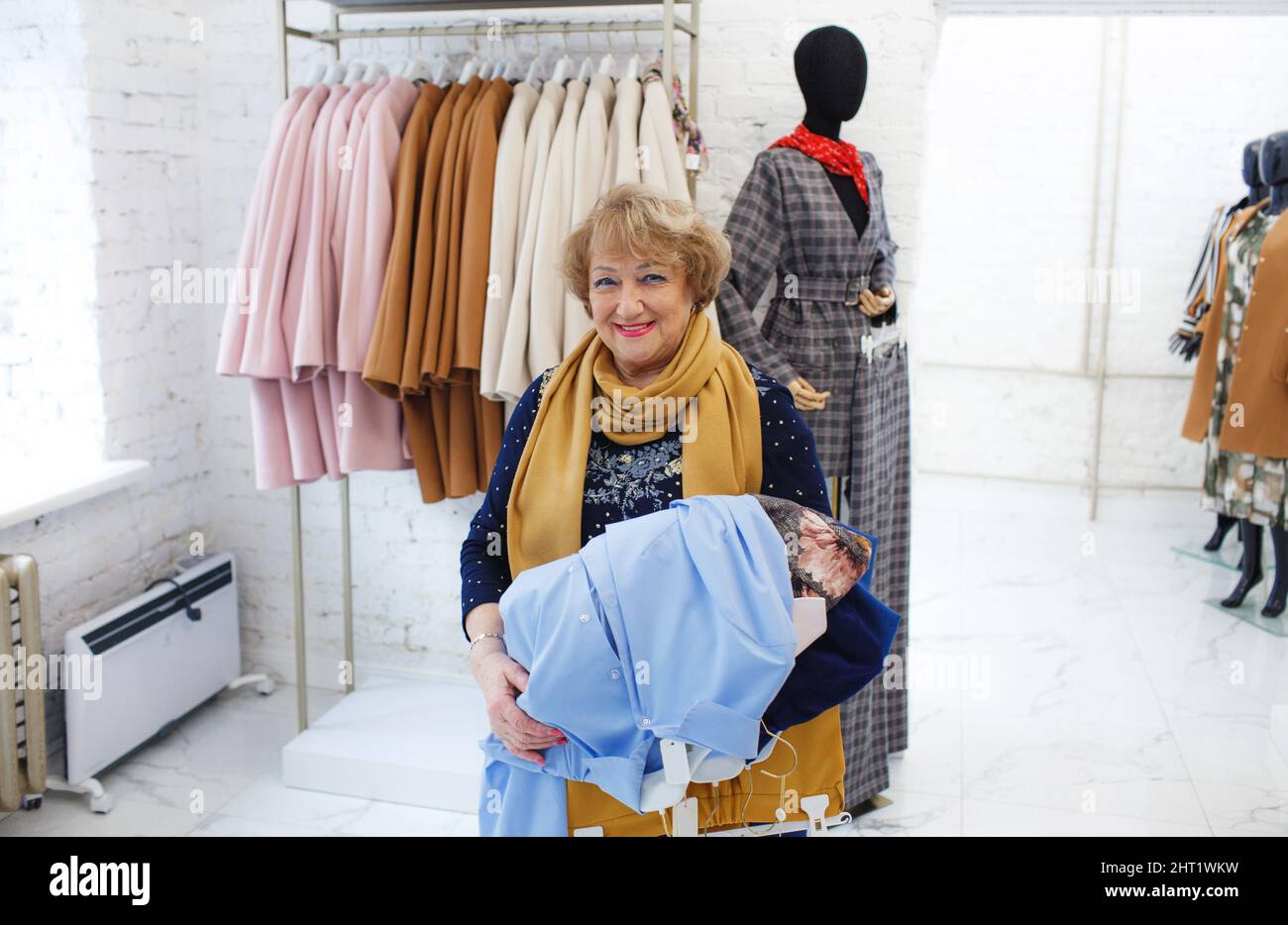 An elderly woman is holding a lot of clothes in her hands getting ready ...