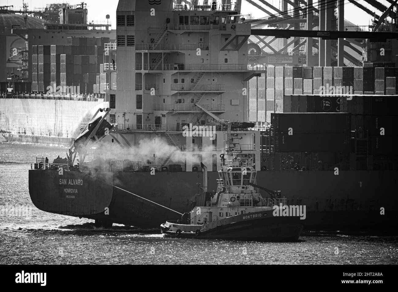 Practical boat pulling a rope to guide and park the big cargo ship on a ...