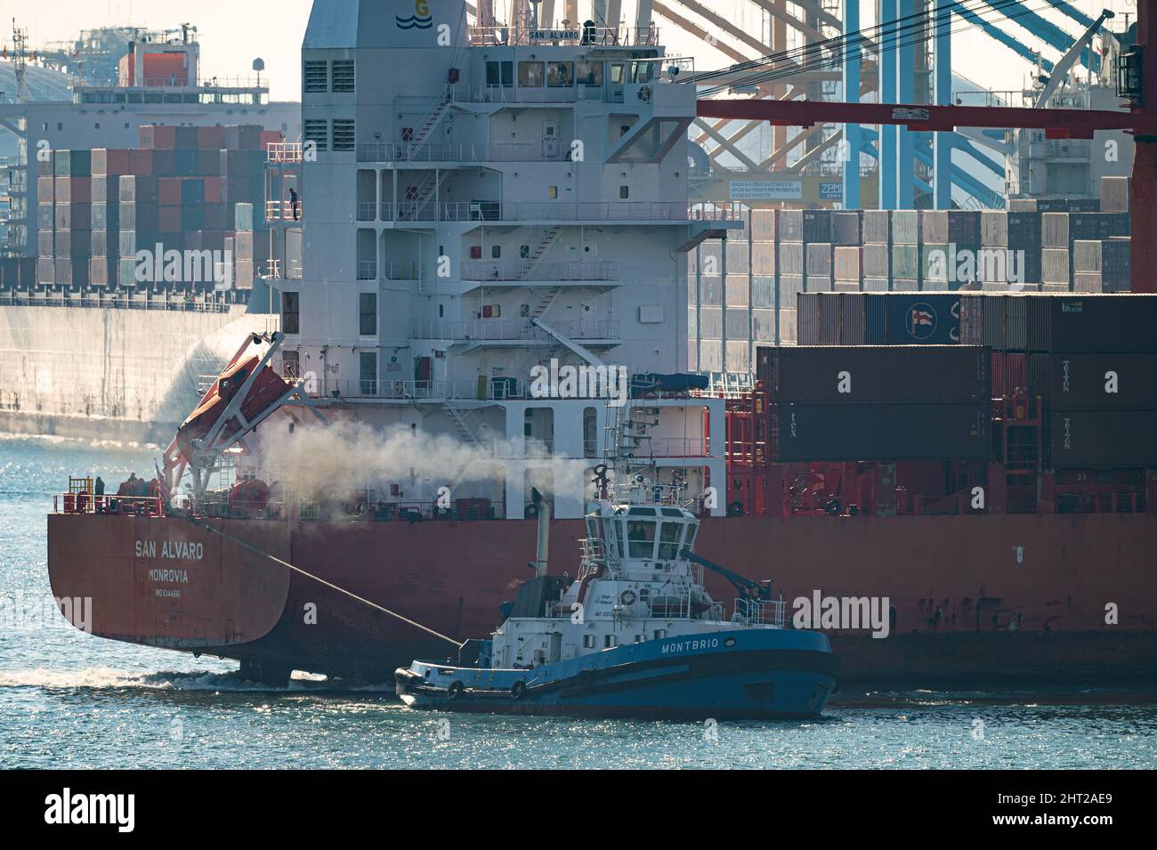 Practical boat pulling a rope to guide and park the big cargo ship ...