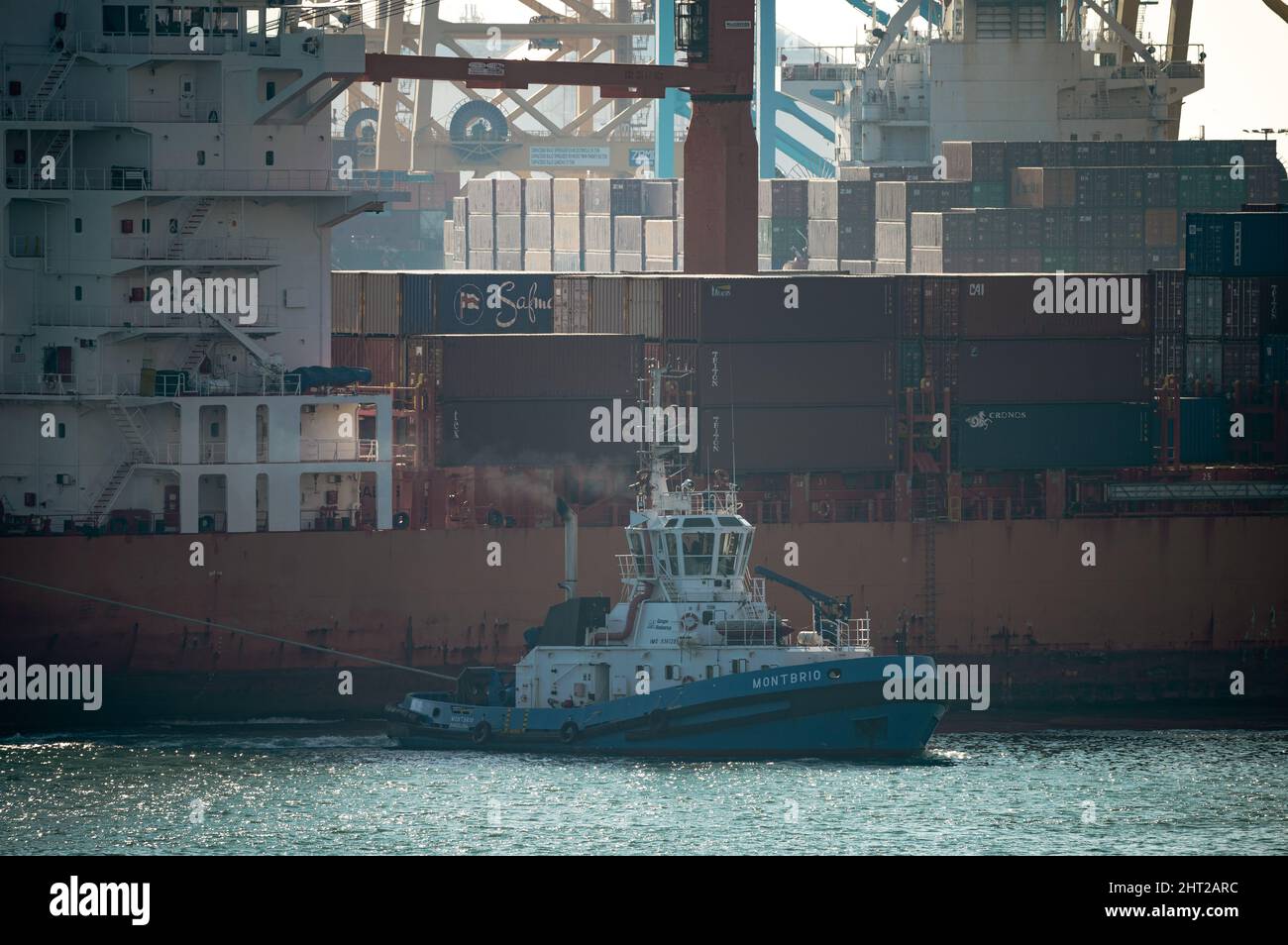 Practical boat pulling a rope to guide and park the big cargo ship ...