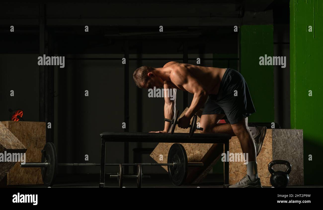 Good looking young man doing triceps dumbbell kickback exercises with ...