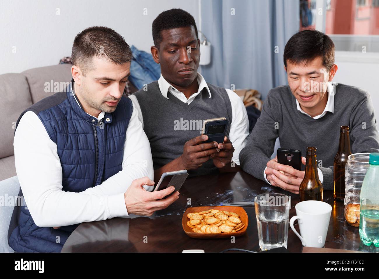 Three friends are chatting each in his phone while relaxing together ...