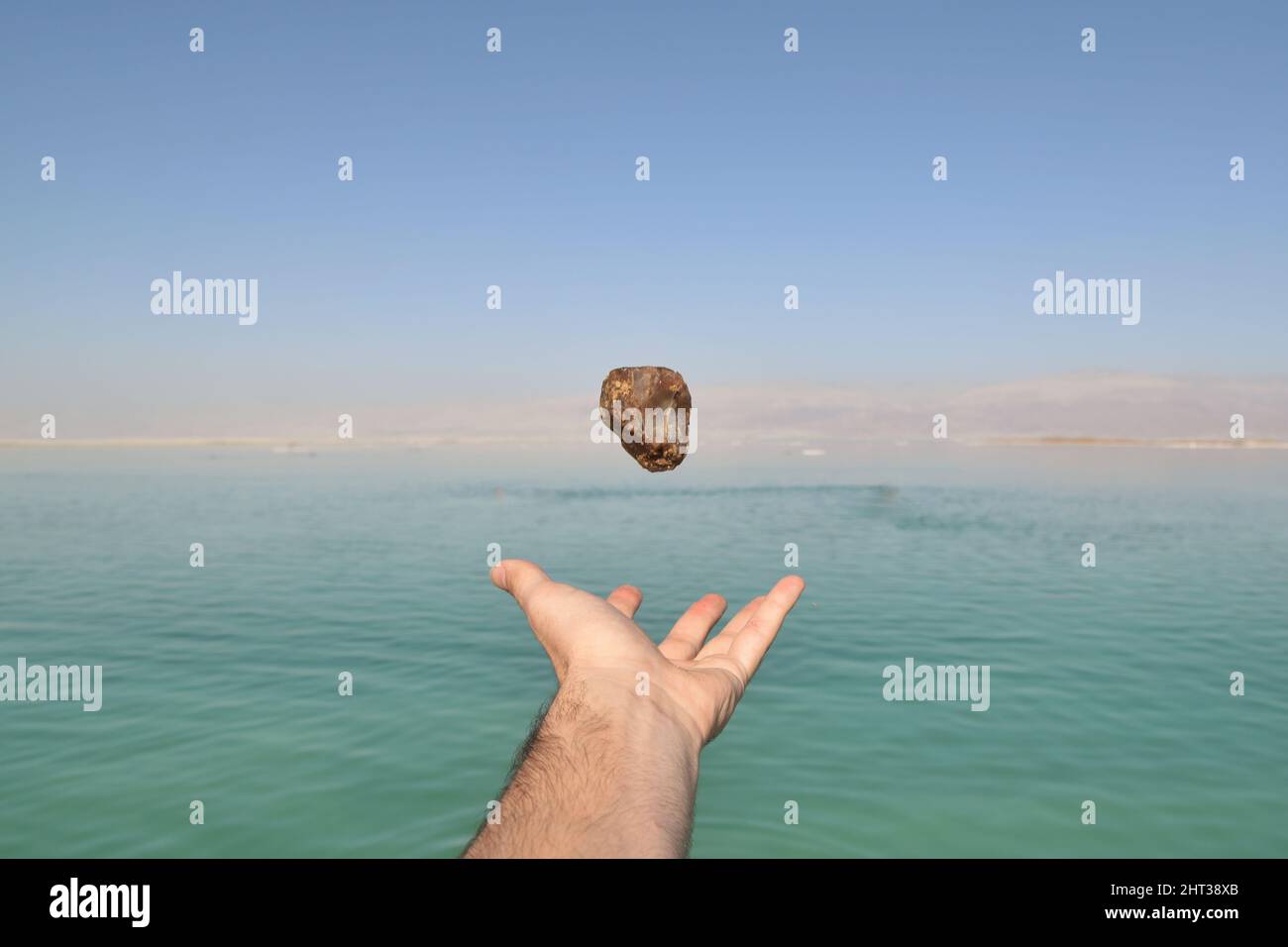 Hand throwing up a rock over a blue sea Stock Photo - Alamy