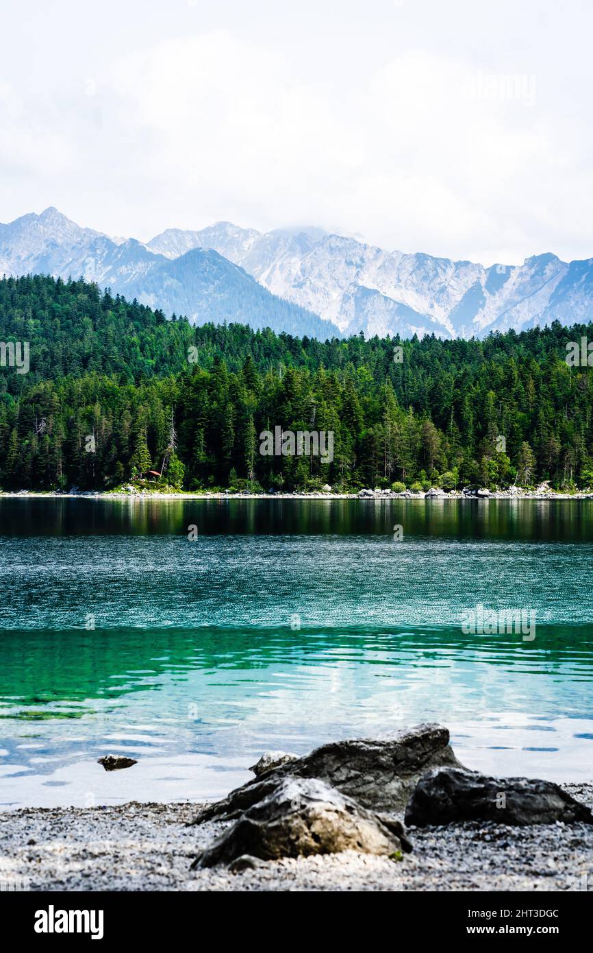 Vertical shot of a calming view of a blue lake with trees and mountains ...