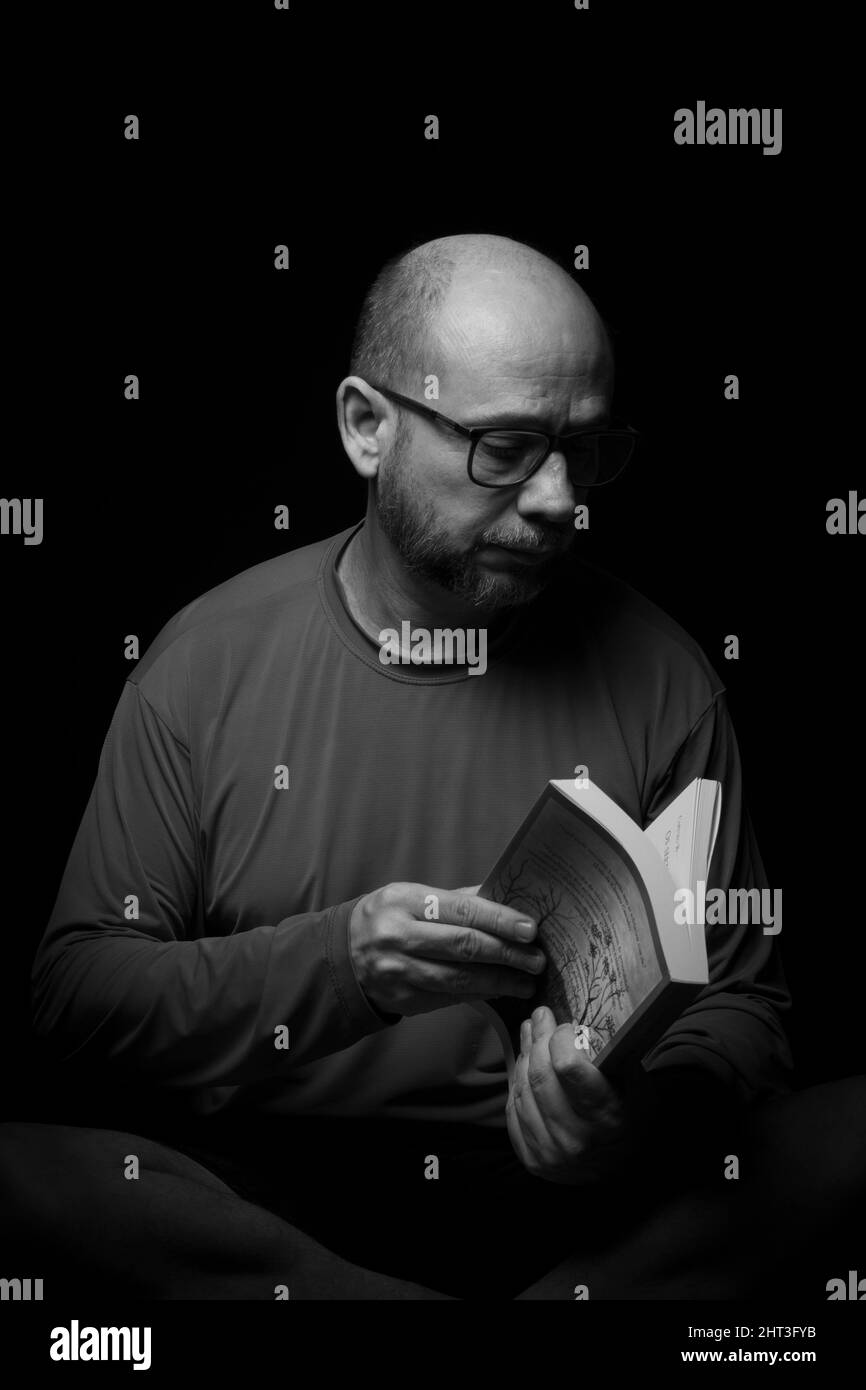 Portrait of a bearded, bald man reading a book against black background ...