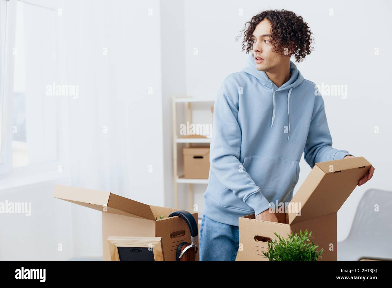 handsome guy in headphones unpacking with box in hand sorting things ...