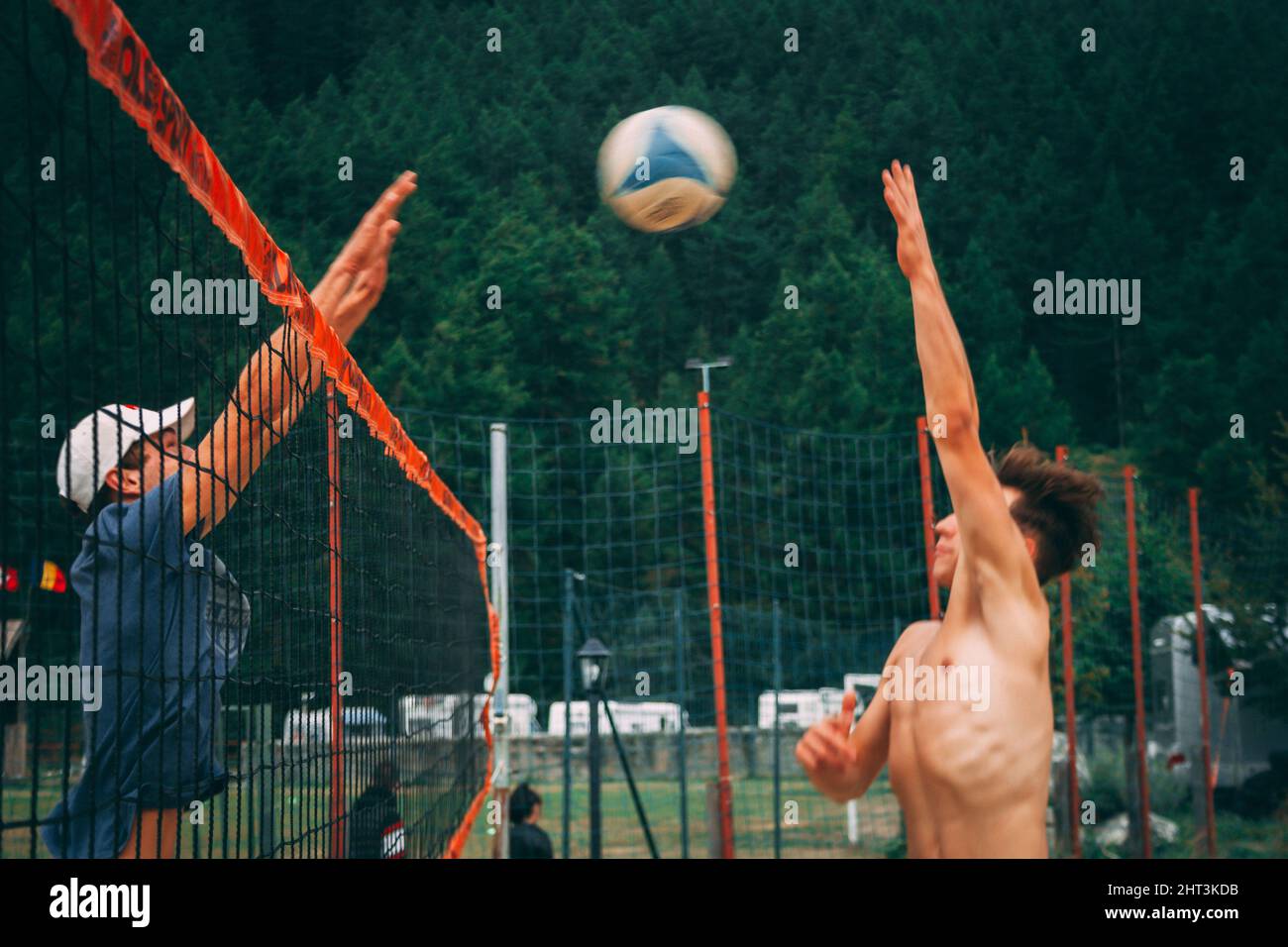Side view of two males playing volleyball in the field against a ...