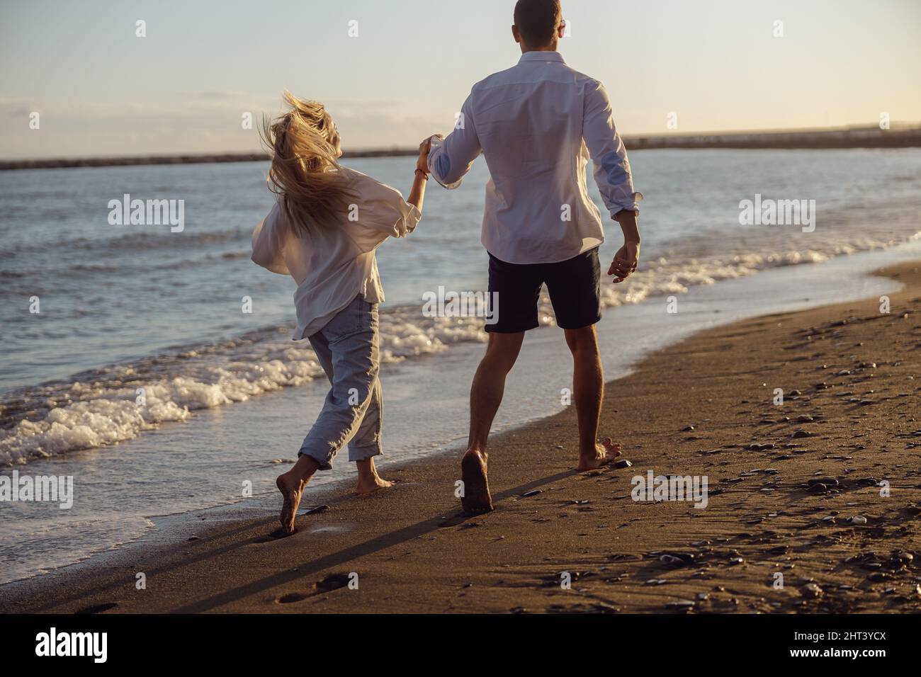 Back photo of couple running along the ocean Stock Photo - Alamy