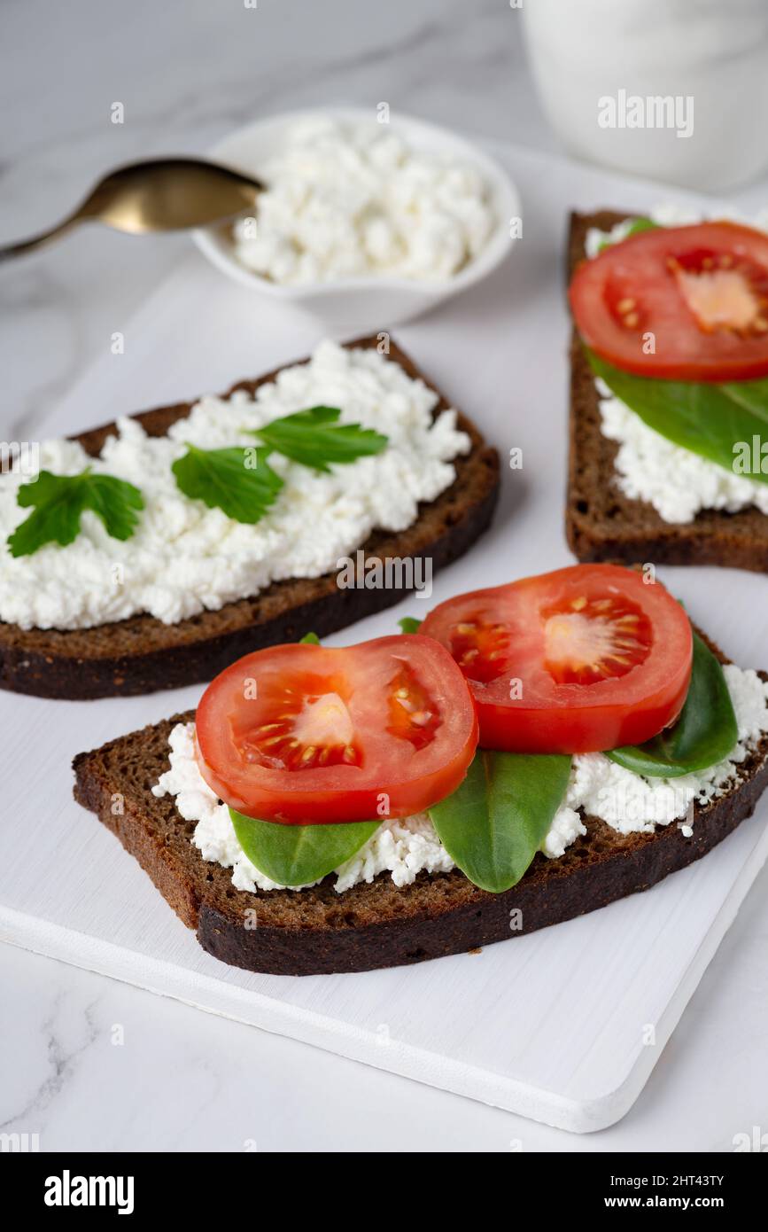 Slice of rye bread with cottage cheese and tomatoes on a wooden cutting ...