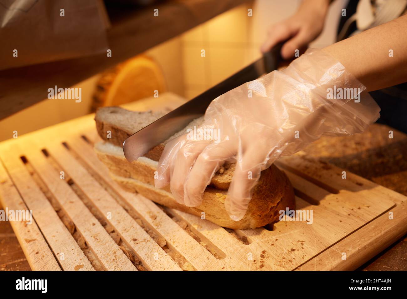 Male hands cutting wheaten bread on the wooden board, selective focus ...