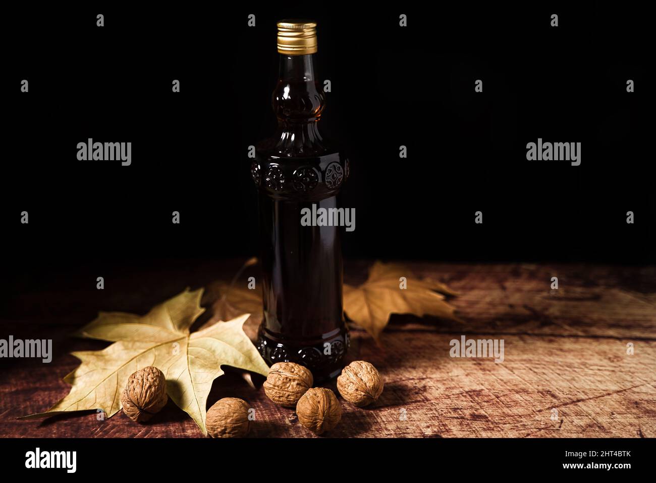 A bottle of walnut wine inserted on a wooden table that has walnuts and ...
