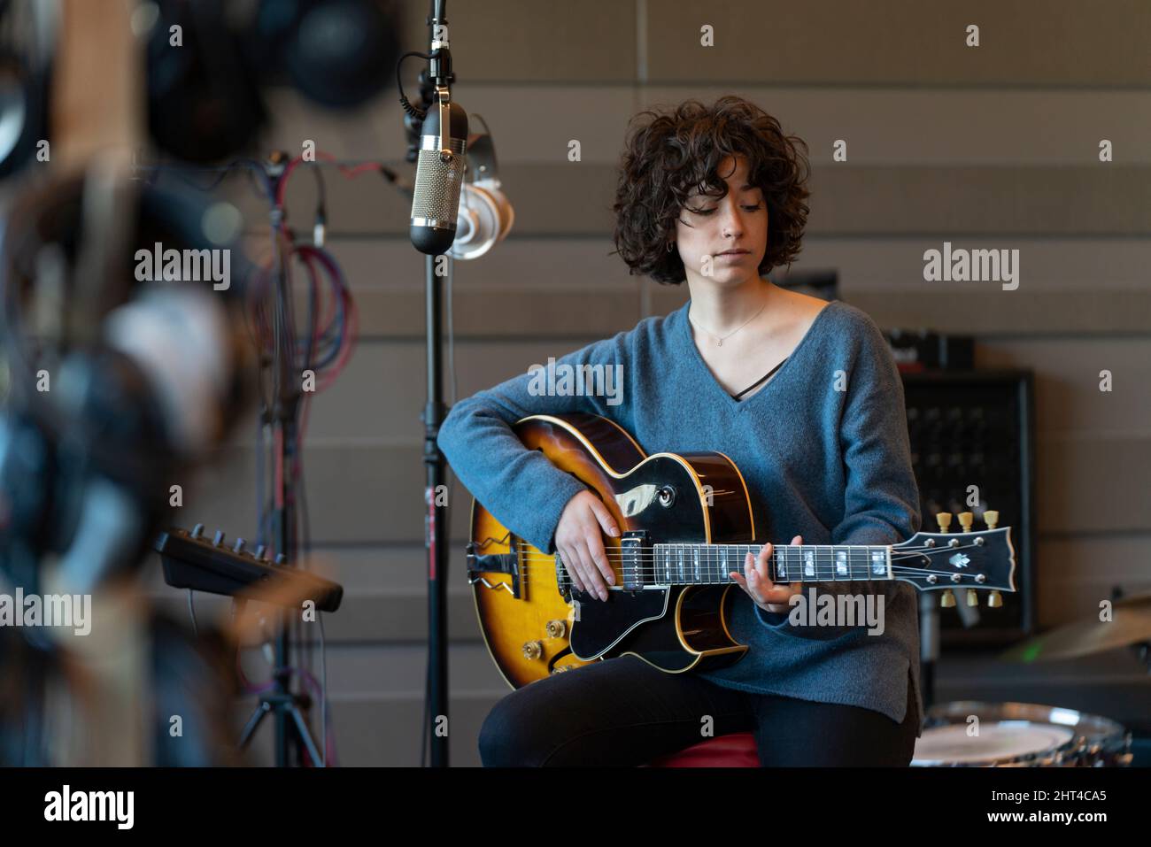 A young singer woman recording a song in a real messy studio with her ...