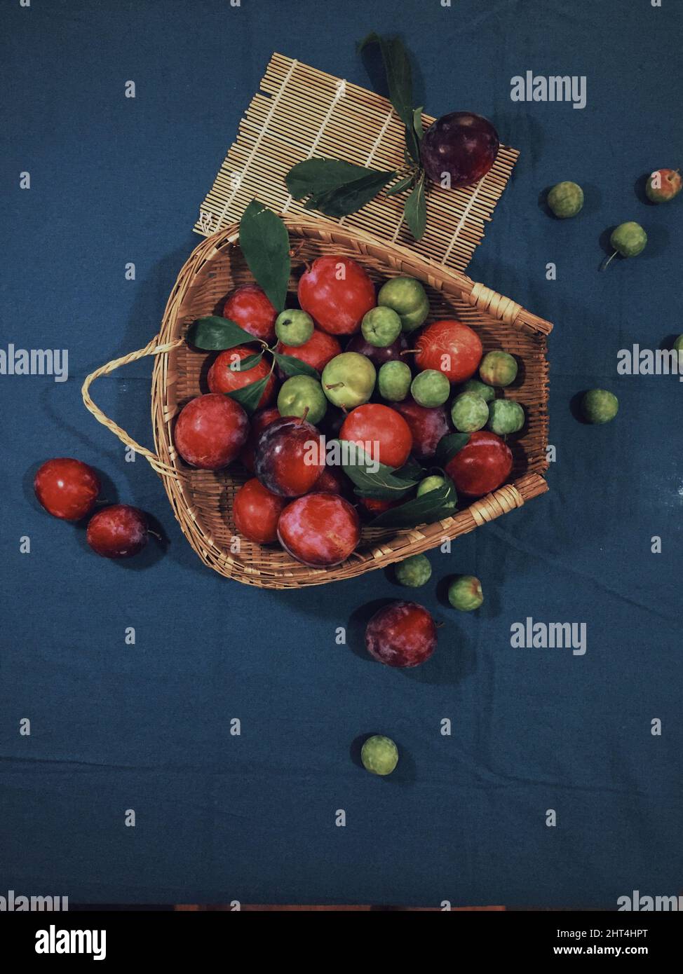 Vertical top view of colorful plums in a straw basket on a blue ...
