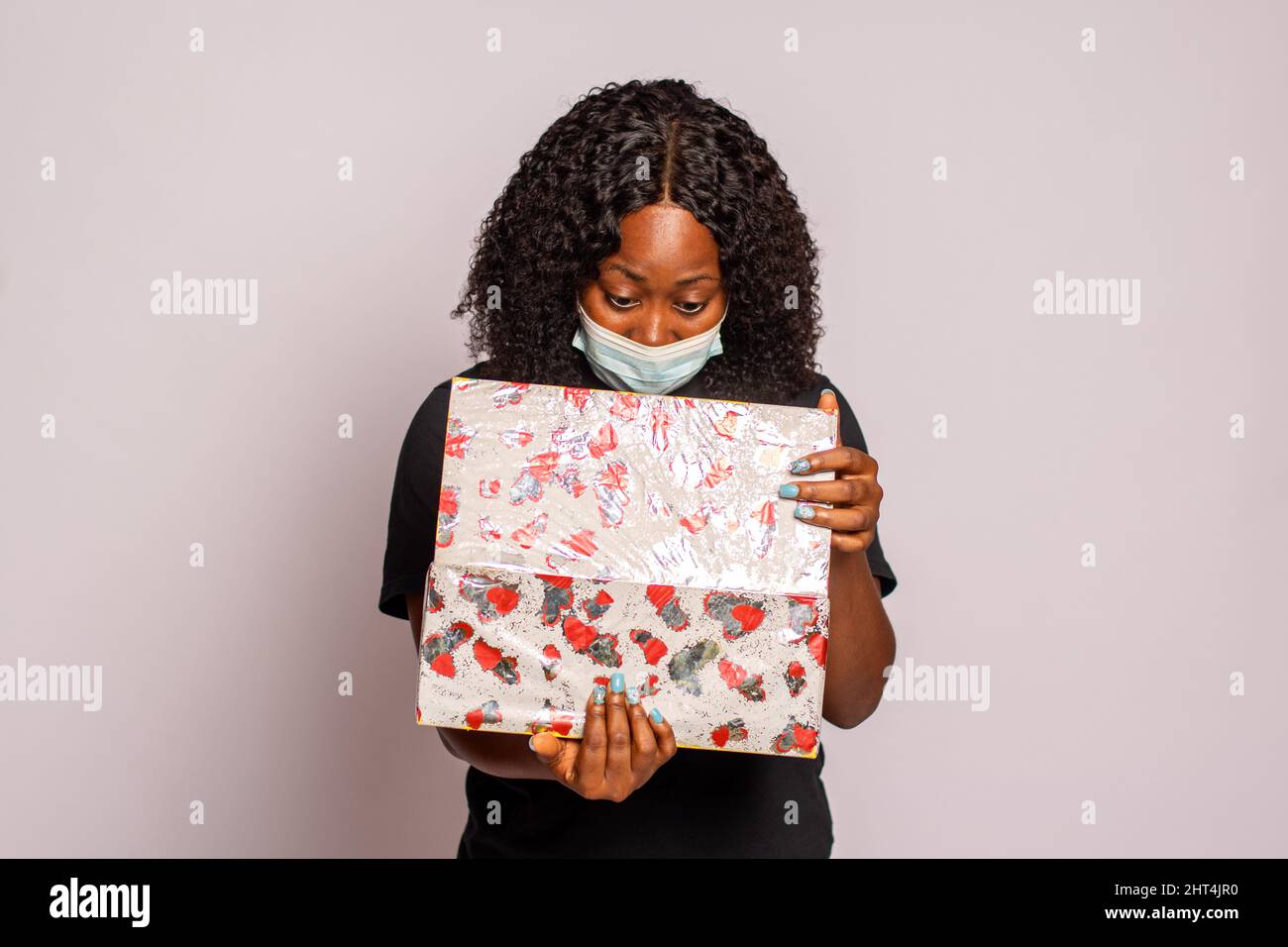 Young black woman wearing a face mask looks inside a gift box Stock ...