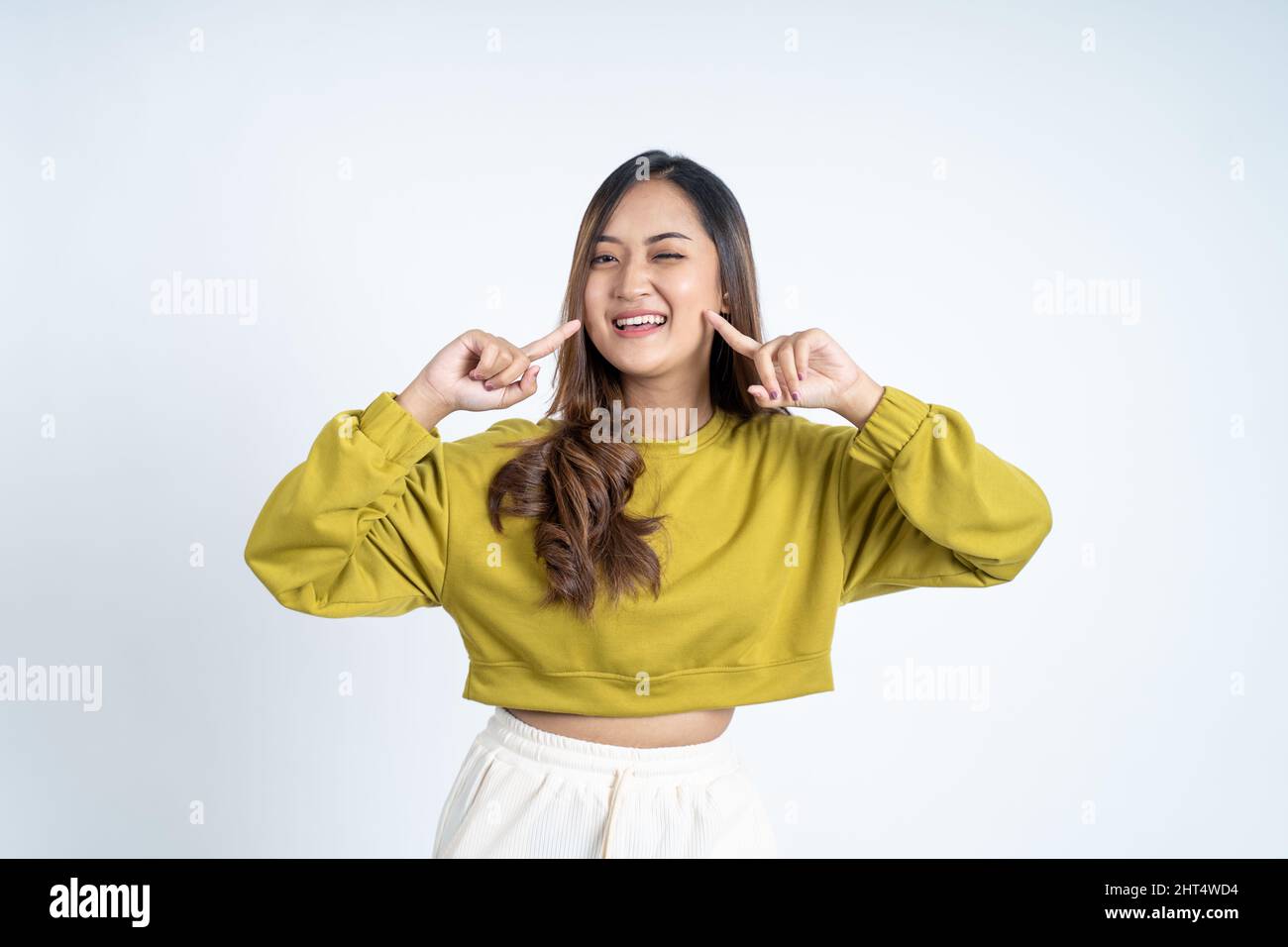 Smiling cute young woman with two fingers pointing to cheek Stock Photo ...