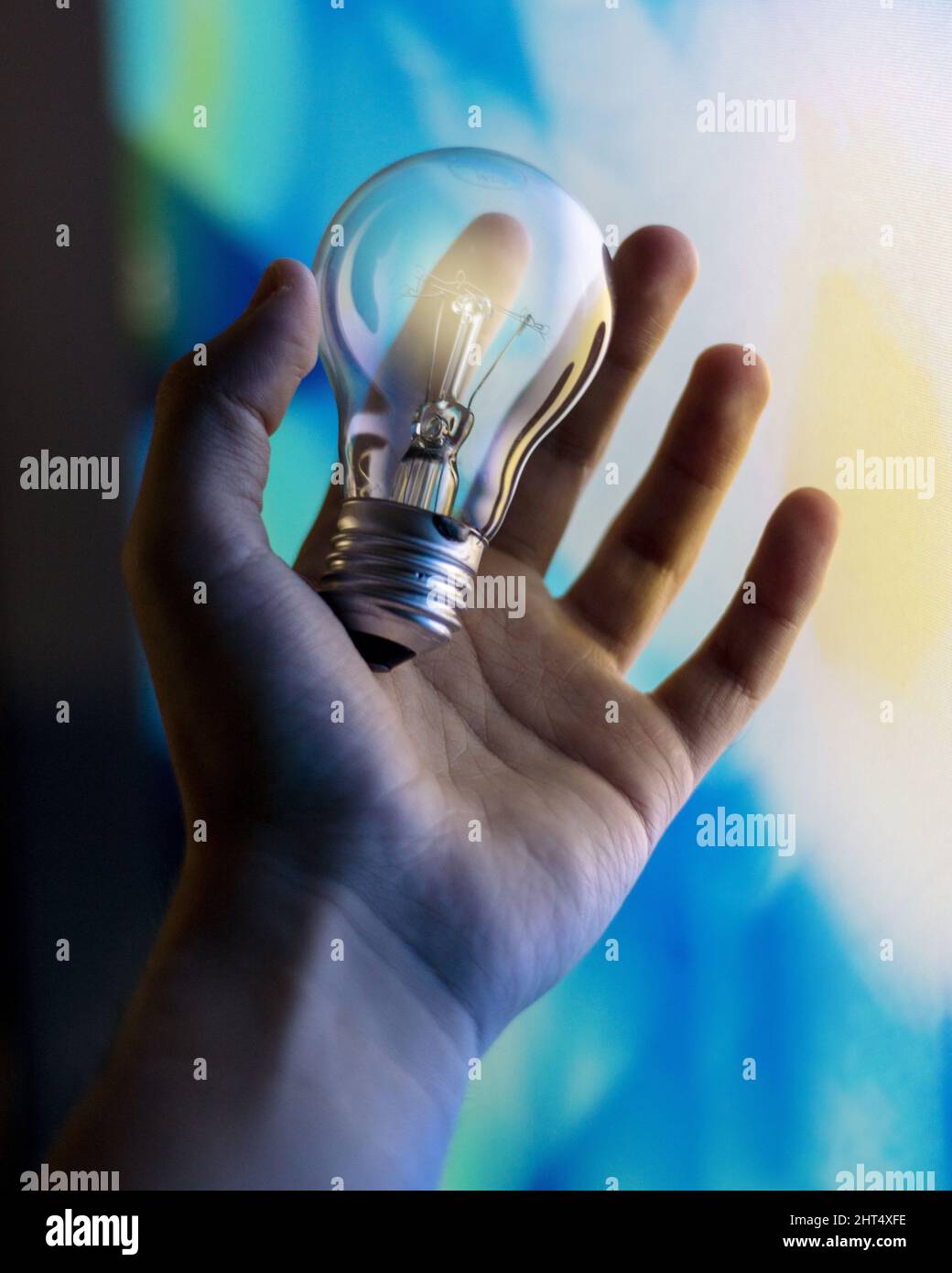 Closeup of a person's hand holding a lightbulb on a blue and yellow ...